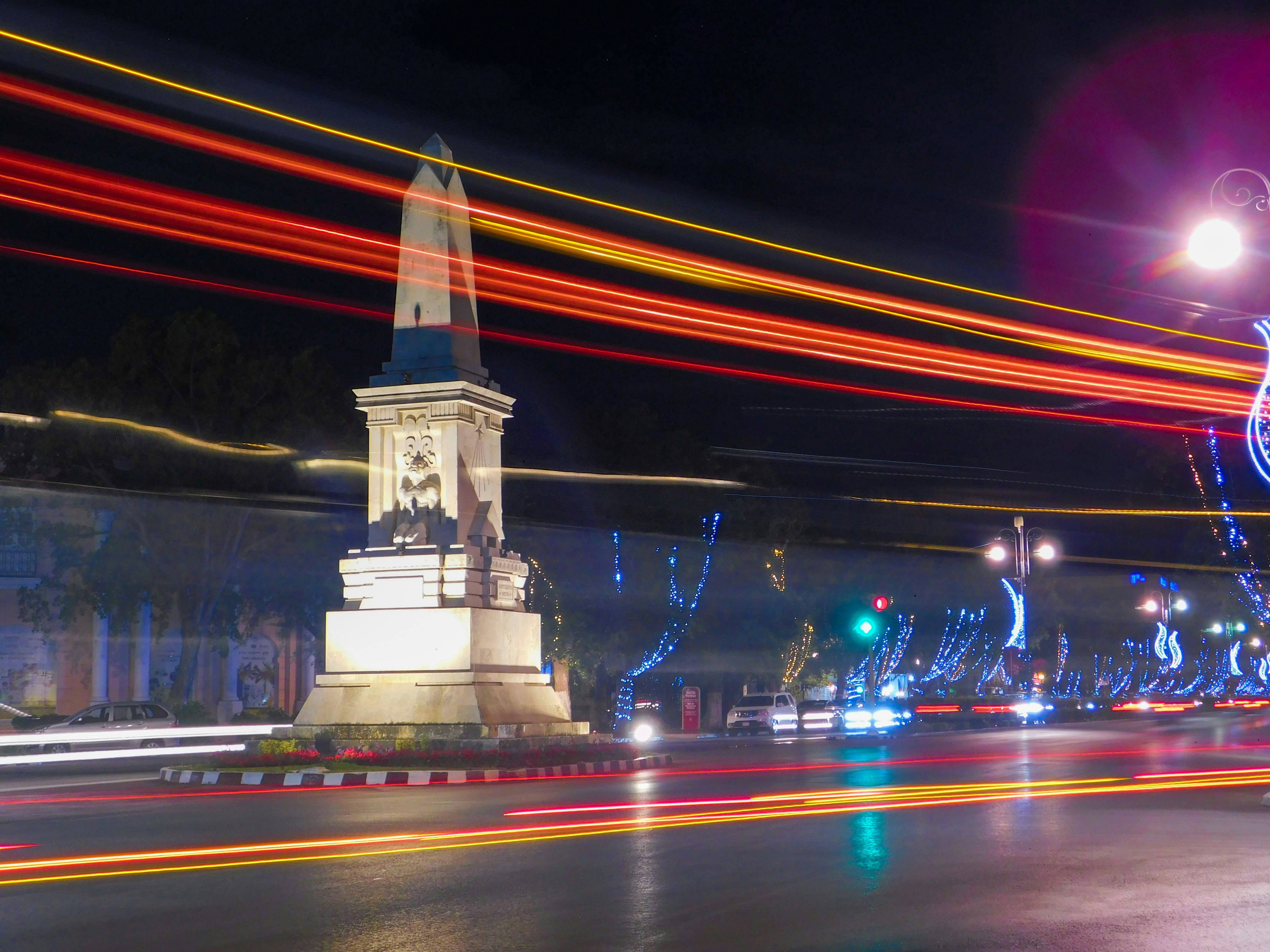 Monument surrounded by colorful light trails from passing vehicles at night.