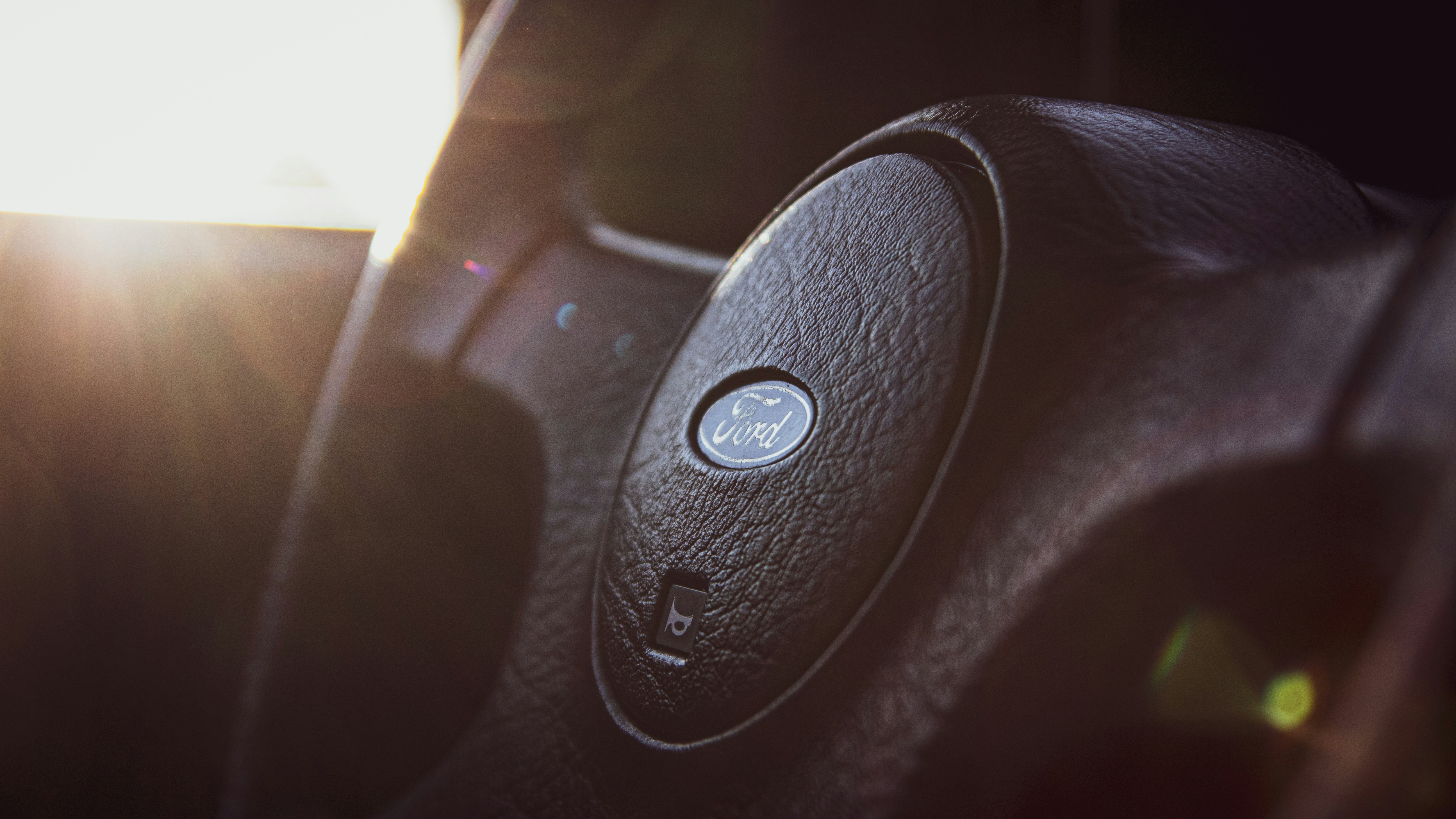 Close-up of a Ford steering wheel with sunlight streaming in, highlighting the textured leather and iconic logo.