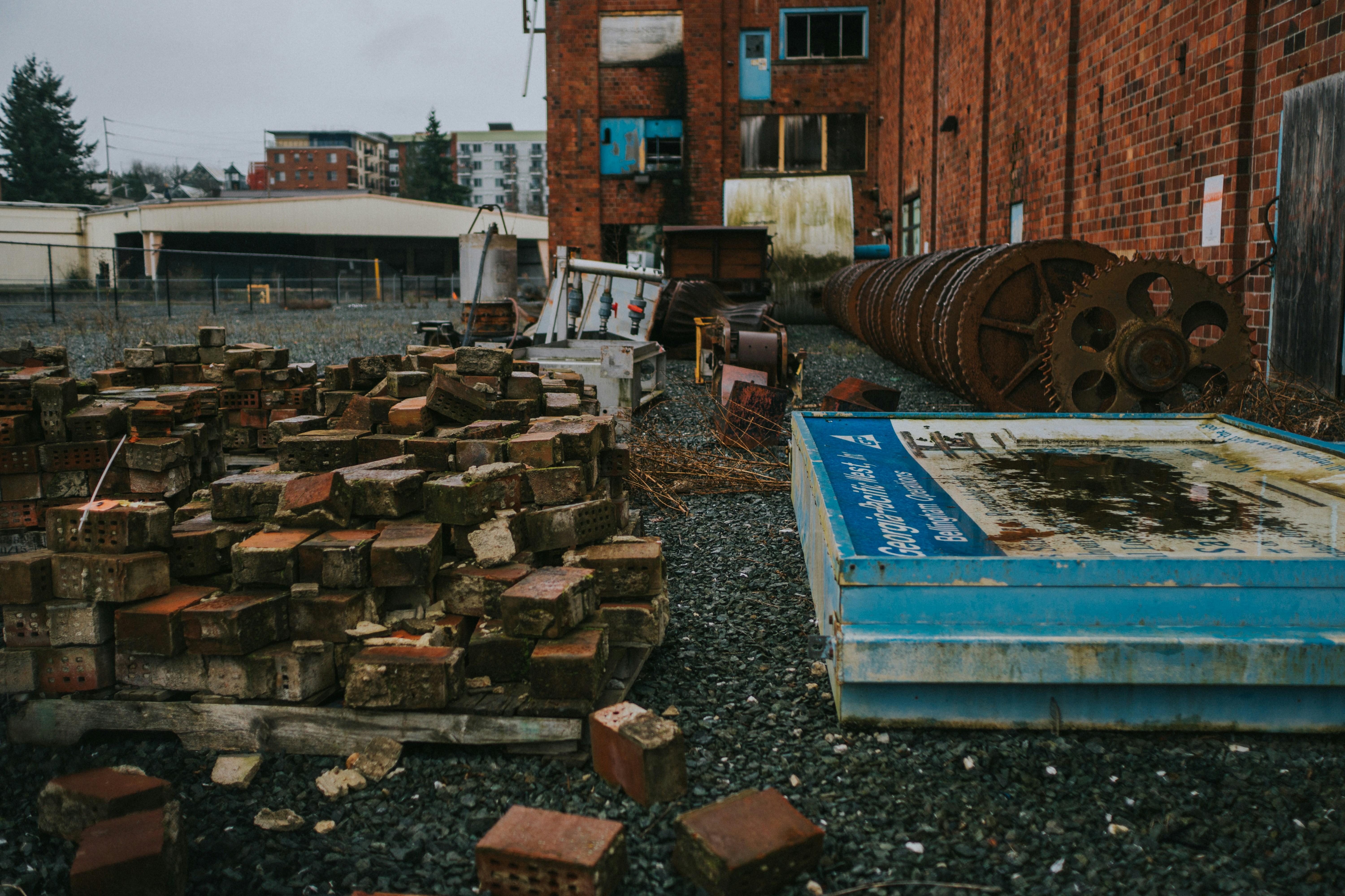 Abandoned industrial site featuring scattered bricks and rusty machinery against a backdrop of a weathered brick building.