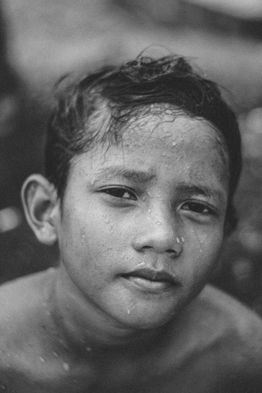 A close-up portrait of a young boy with water droplets on his face, conveying a sense of contemplation and resilience.