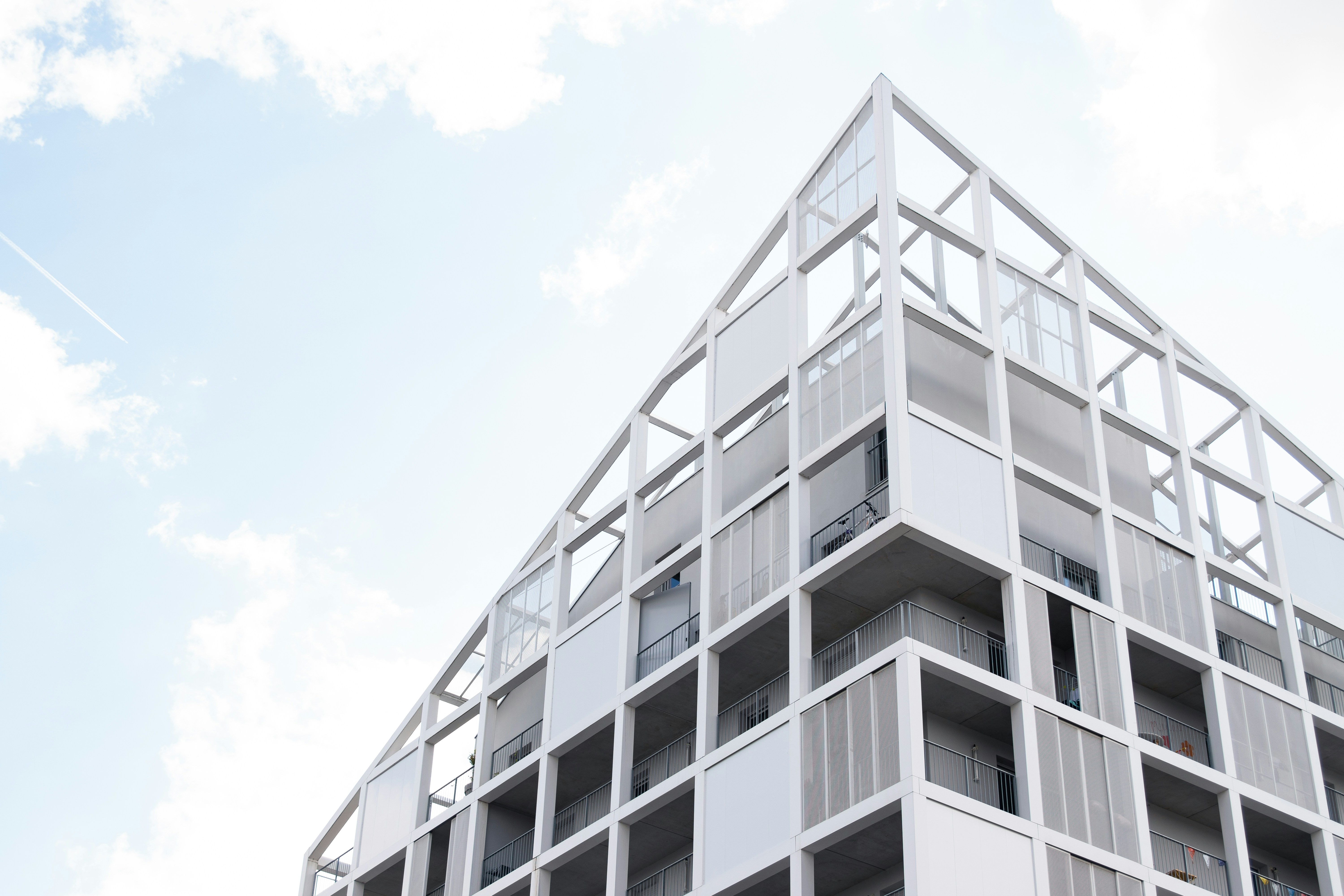 Modern white geometric building with open grid design set against a partly cloudy sky.