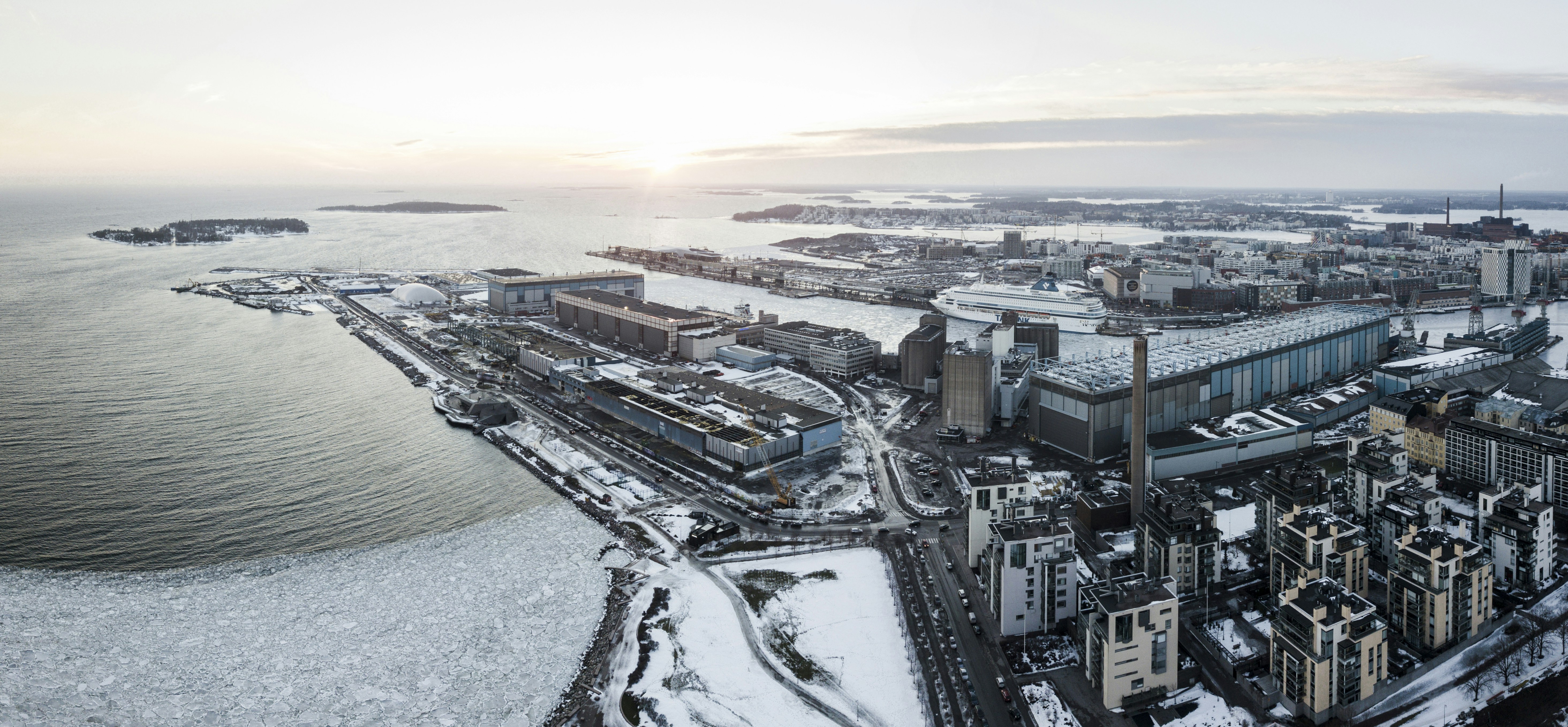 Aerial view of Helsinki's snow-covered cityscape and icy waterfront at sunrise.