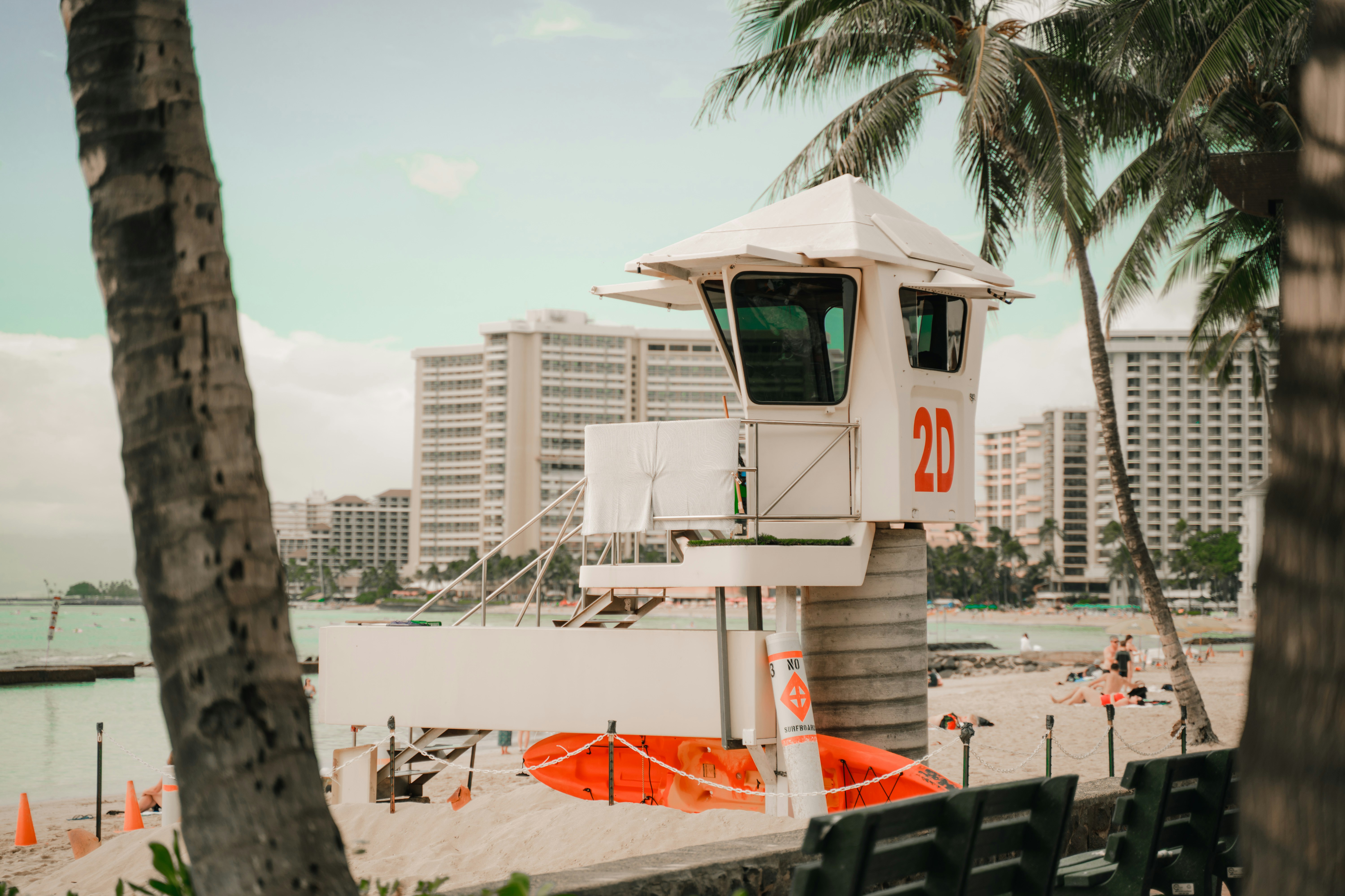 Lifeguard tower overlooking a calm beach with high-rise buildings in the background, framed by palm trees.