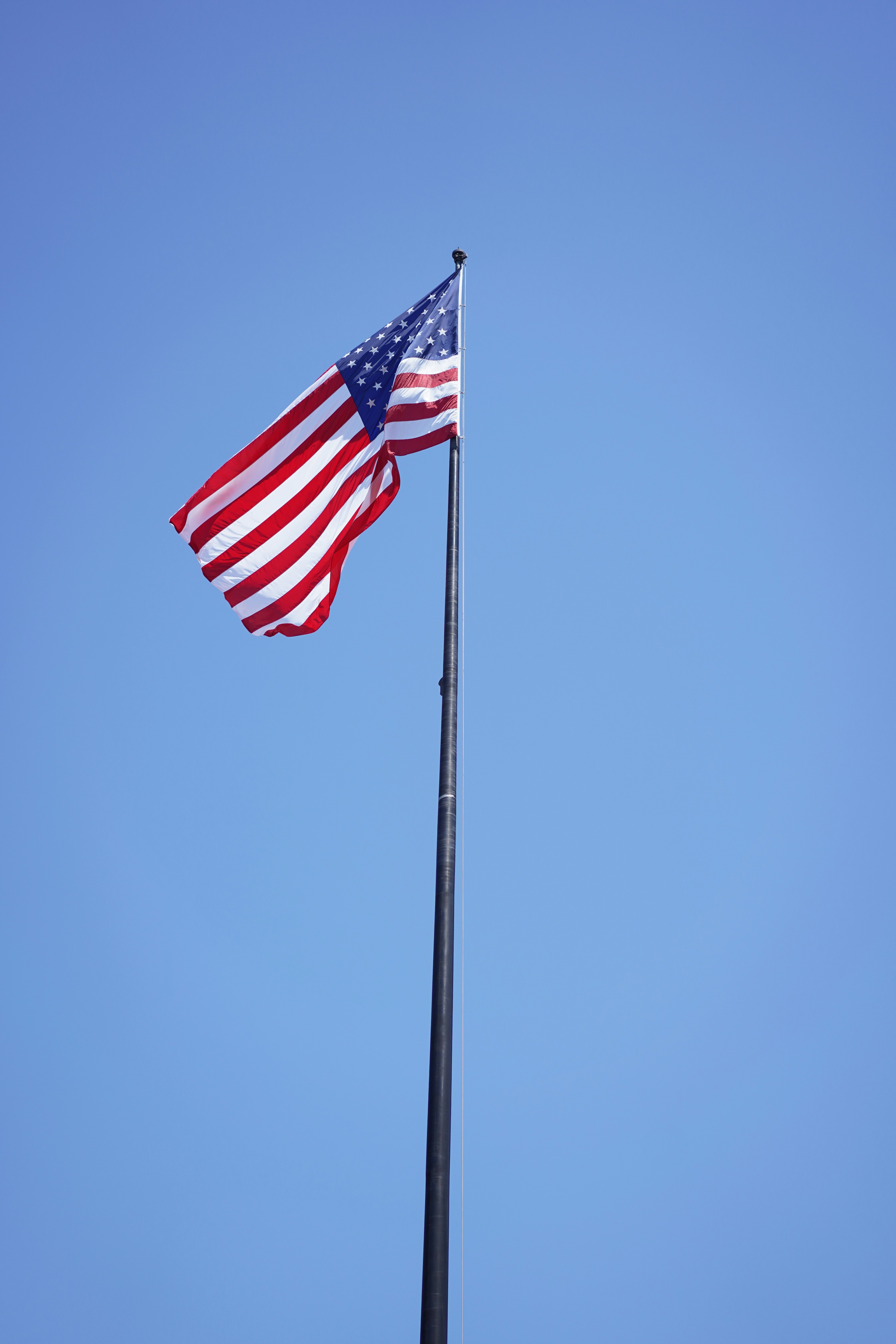 American flag fluttering atop a flagpole under a bright blue sky.
