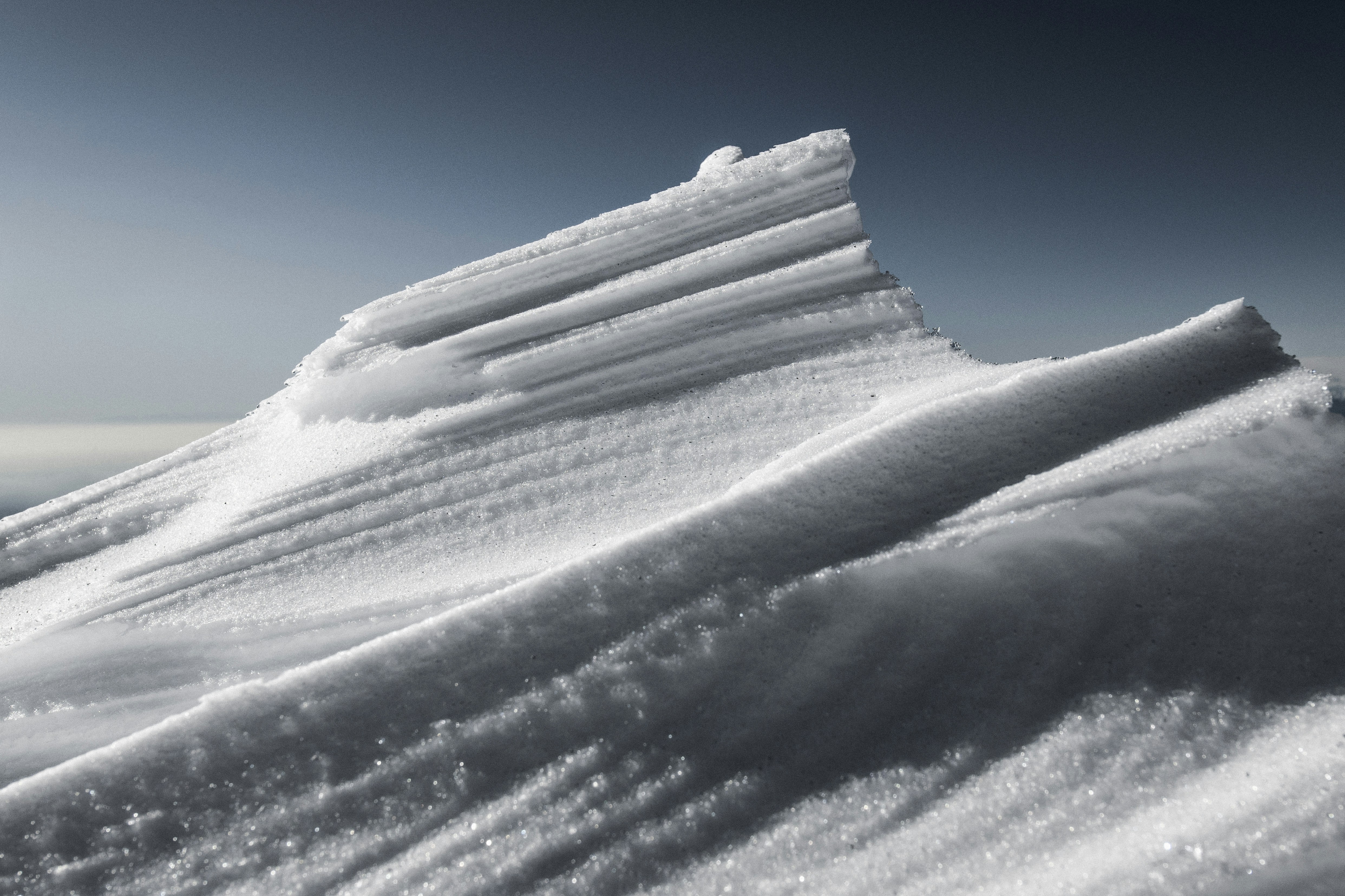 Intricate patterns of snowdrifts shaped by the wind against a clear sky.