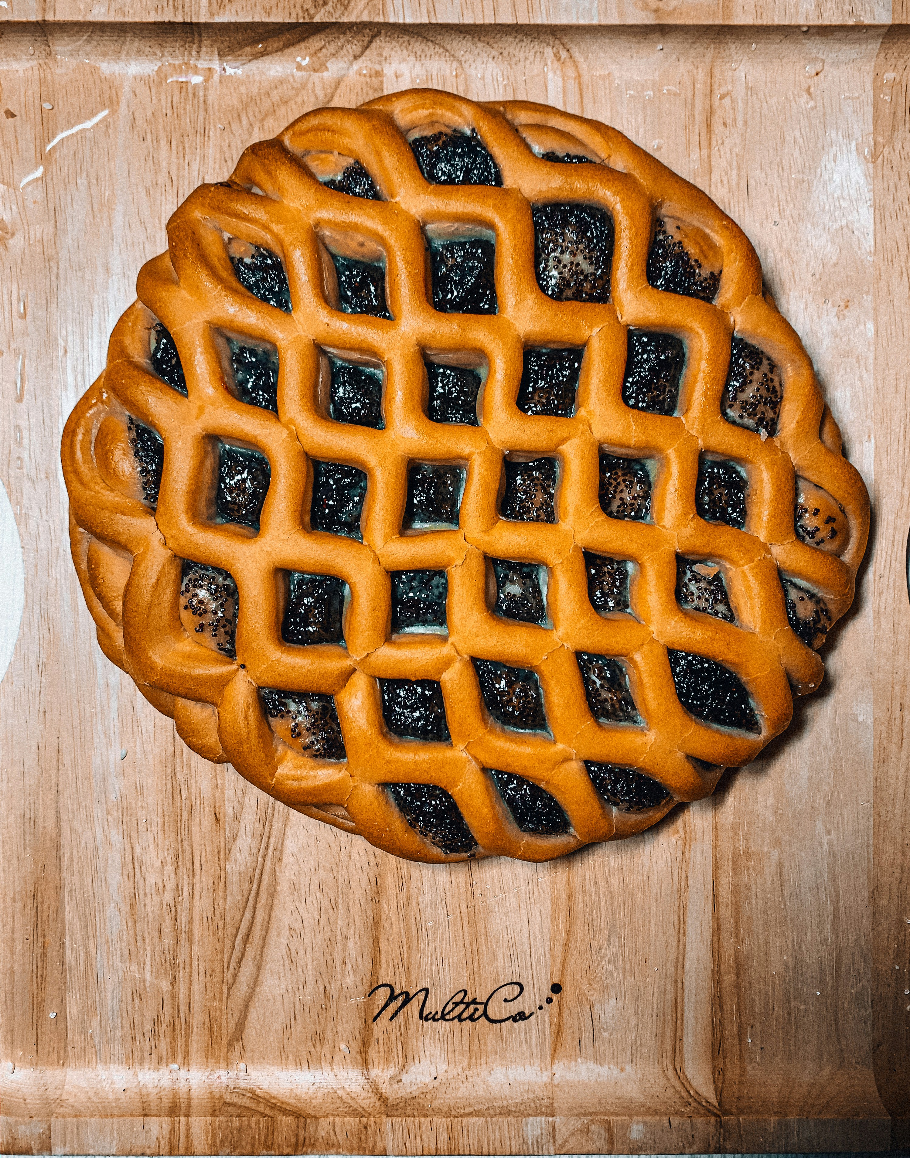 Intricately woven lattice crust encasing a dark filling, presented on a wooden surface.