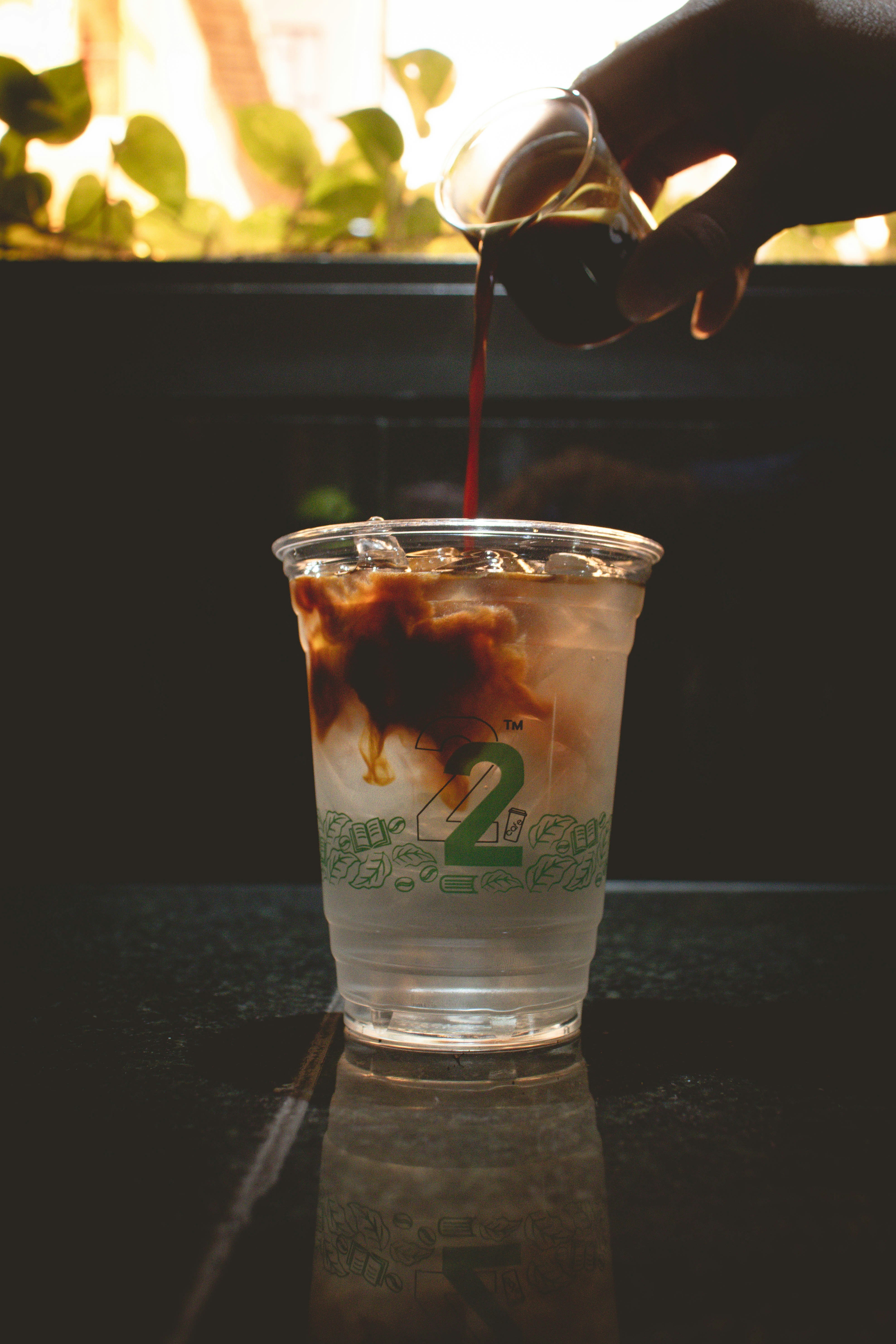 Coffee being poured into a cup filled with ice, creating a swirling pattern. The scene captures the moment of mixology in a casual setting.