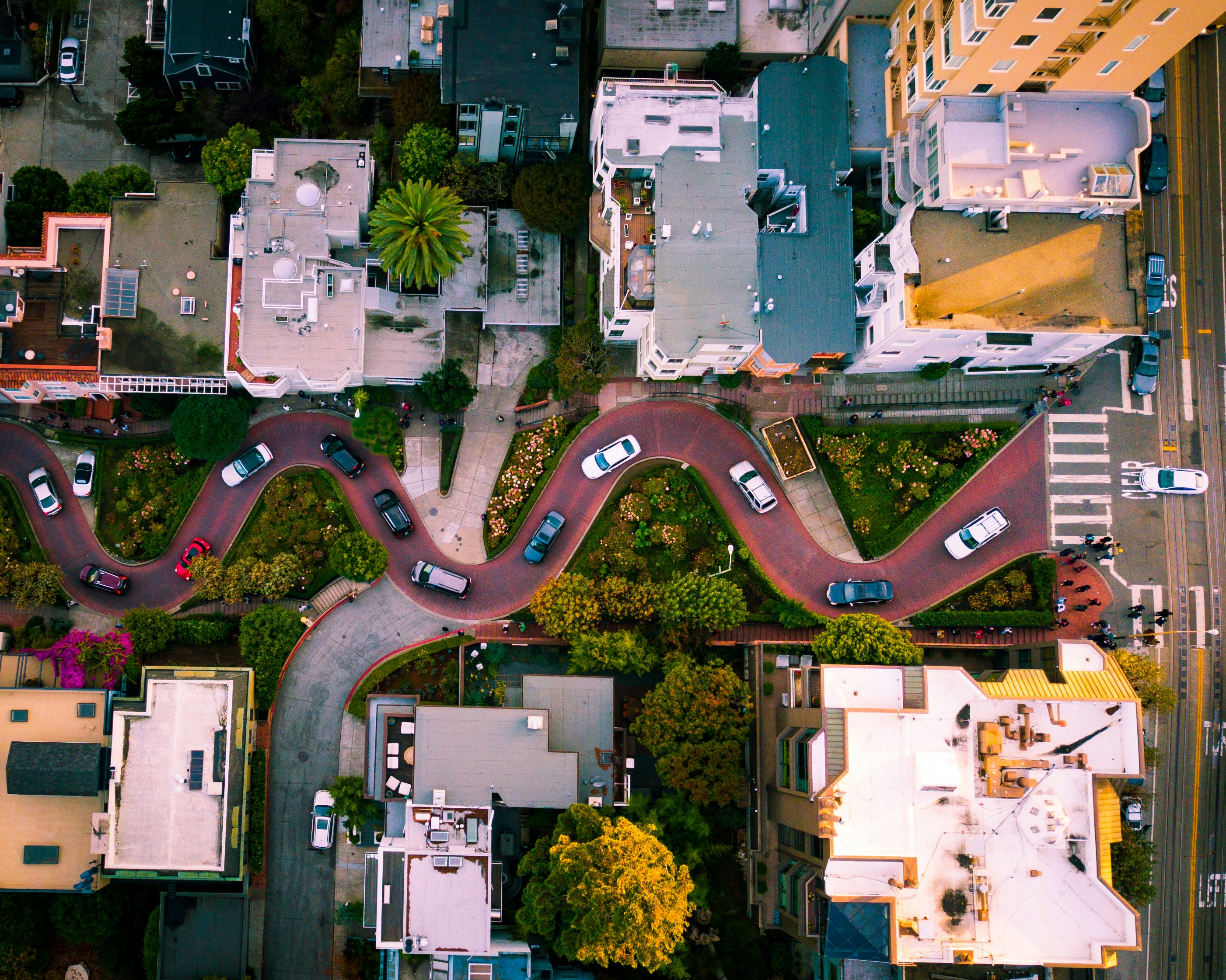 Aerial view of a winding, zigzag street lined with cars and surrounded by urban buildings.