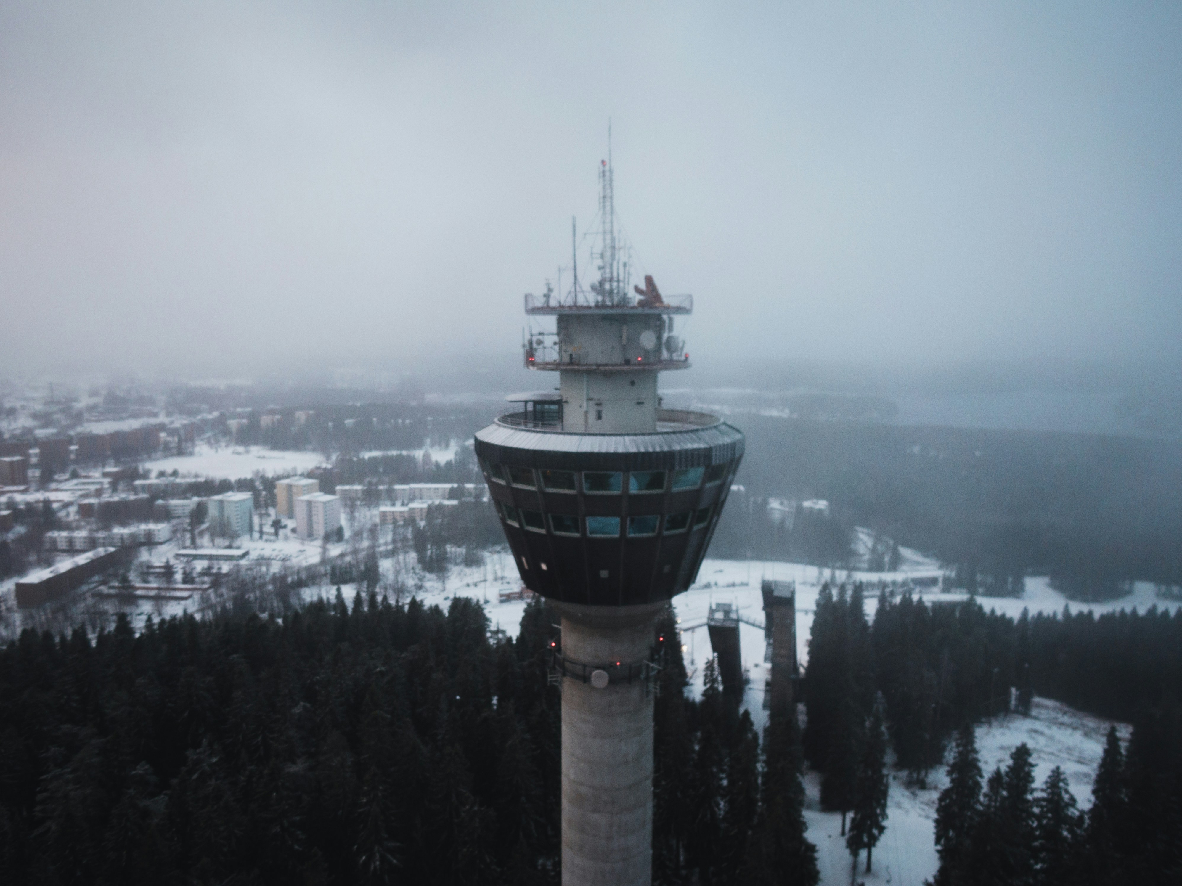 Tall communication tower rising above a snowy forest landscape under an overcast sky.