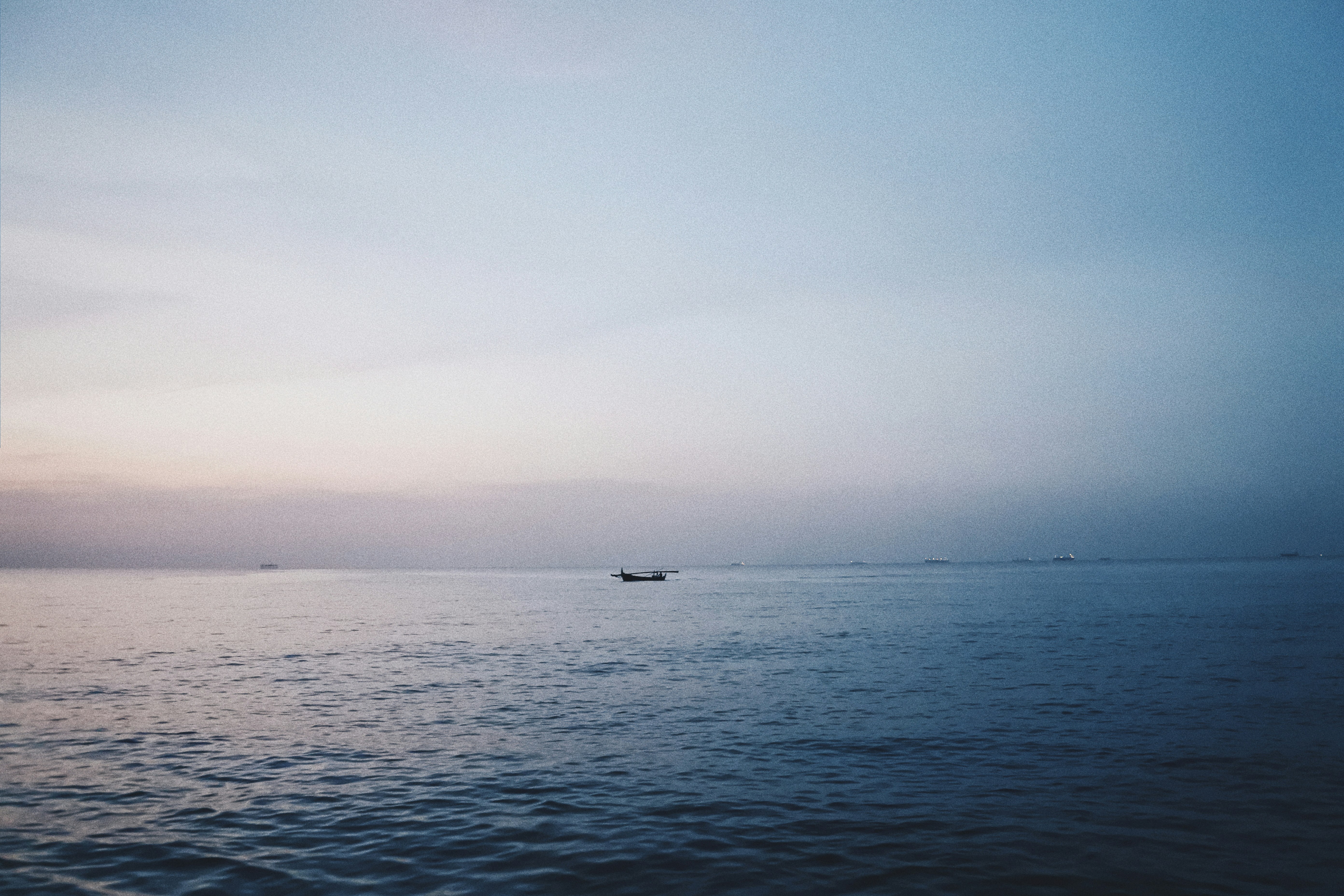 Small boat drifts on calm ocean waters beneath a gradient sky transitioning from soft pink to deep blue.