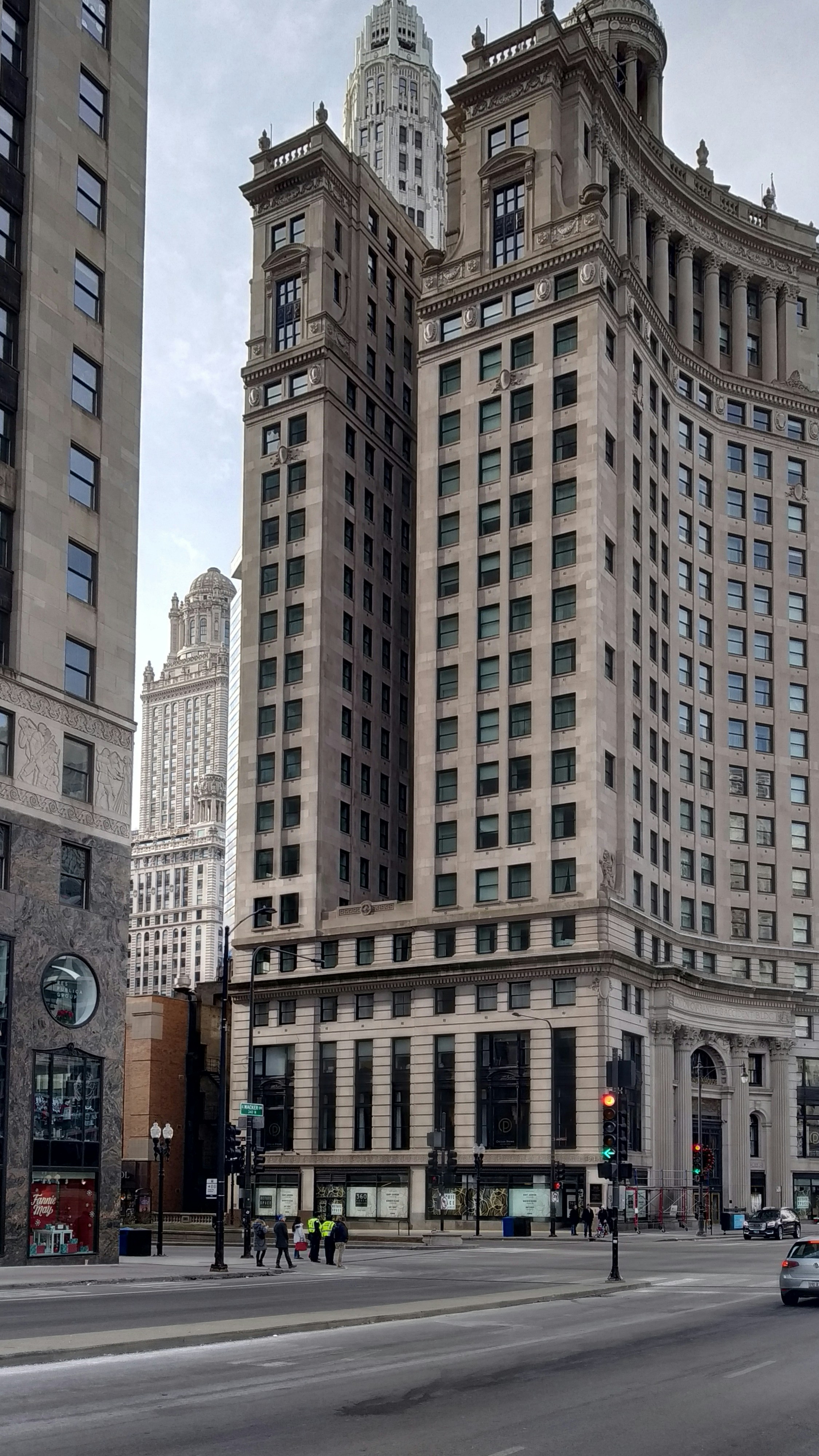 Urban street scene featuring a grand historic building with ornate facade, pedestrians and traffic at the curb, capturing architectural scale and city life.