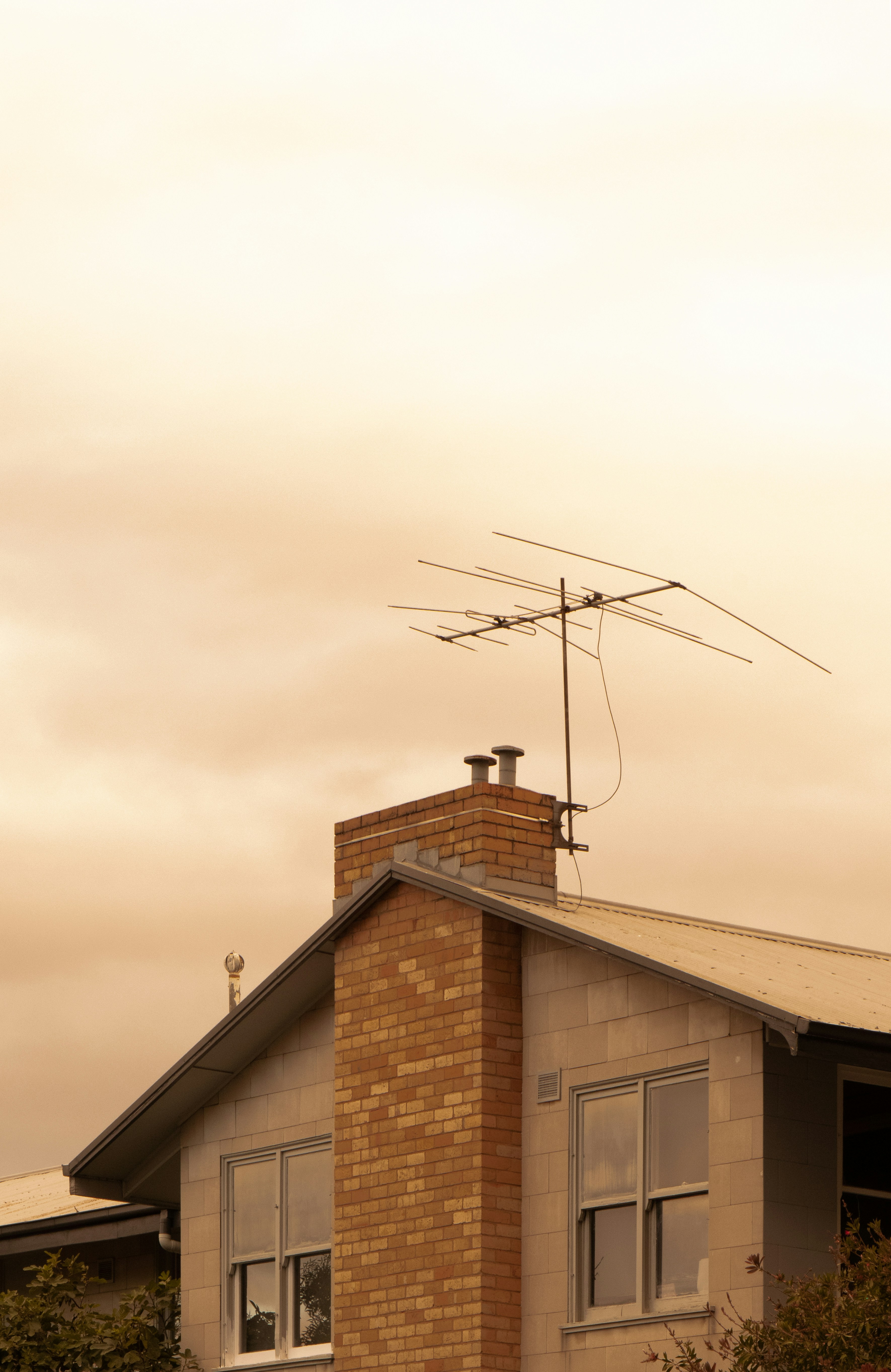 Brick Chimney Serenade: A TV Antenna Against a Gilded Evening Sky