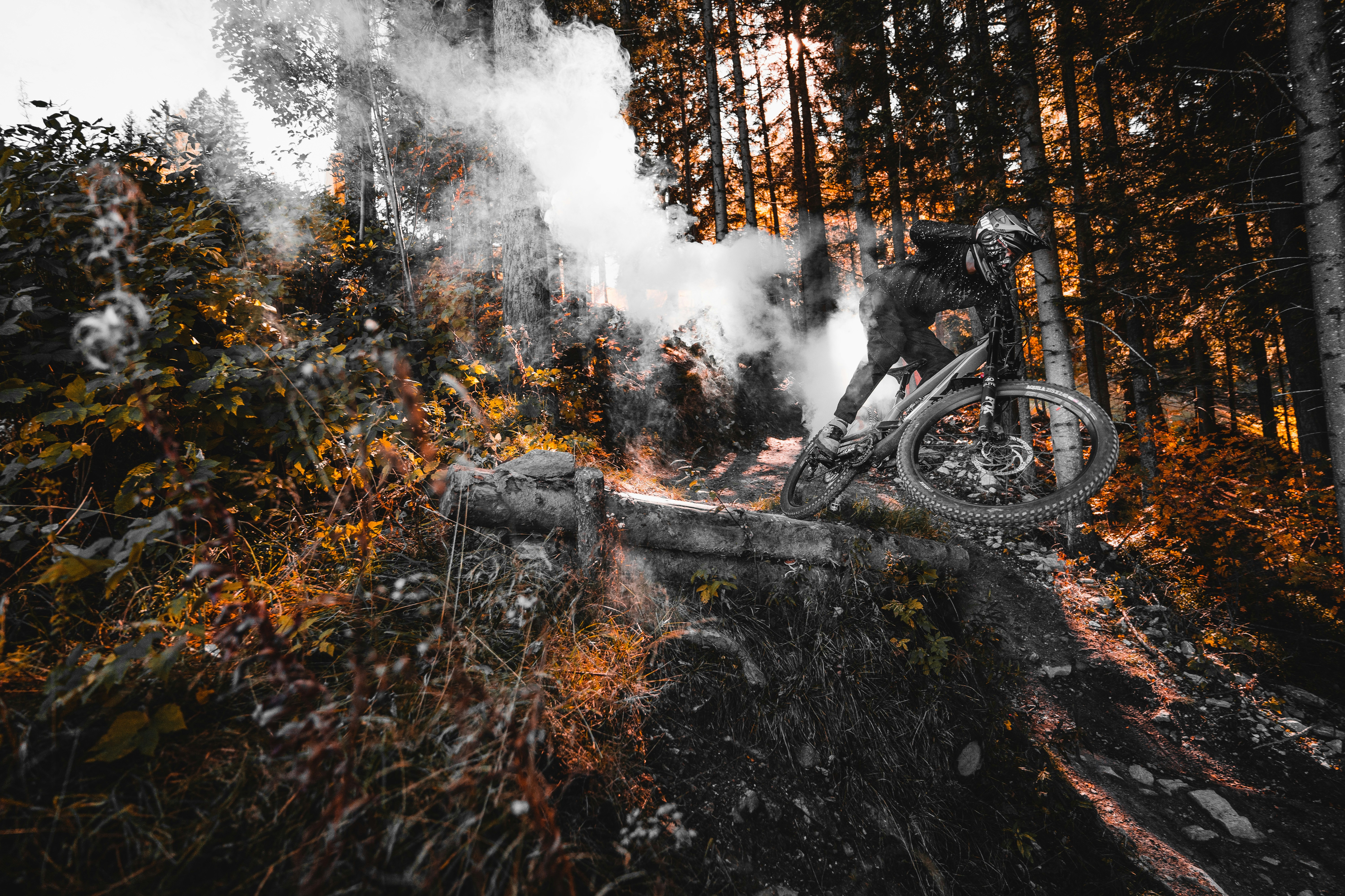 Muddy descent: a rider leaps a log amid smoke and autumn pines