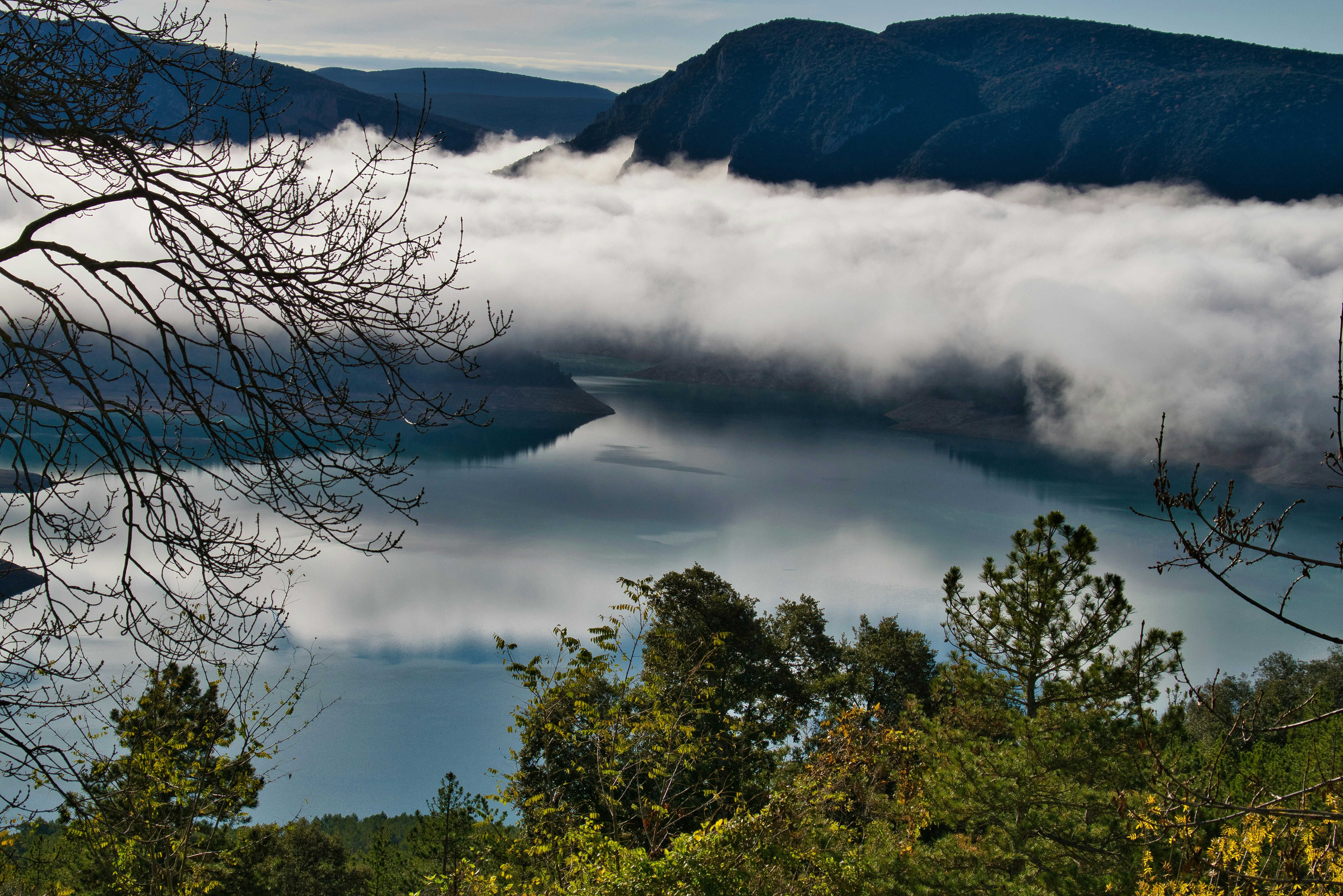 Layer of clouds drapes between mountain peaks, reflecting in the tranquil lake below.
