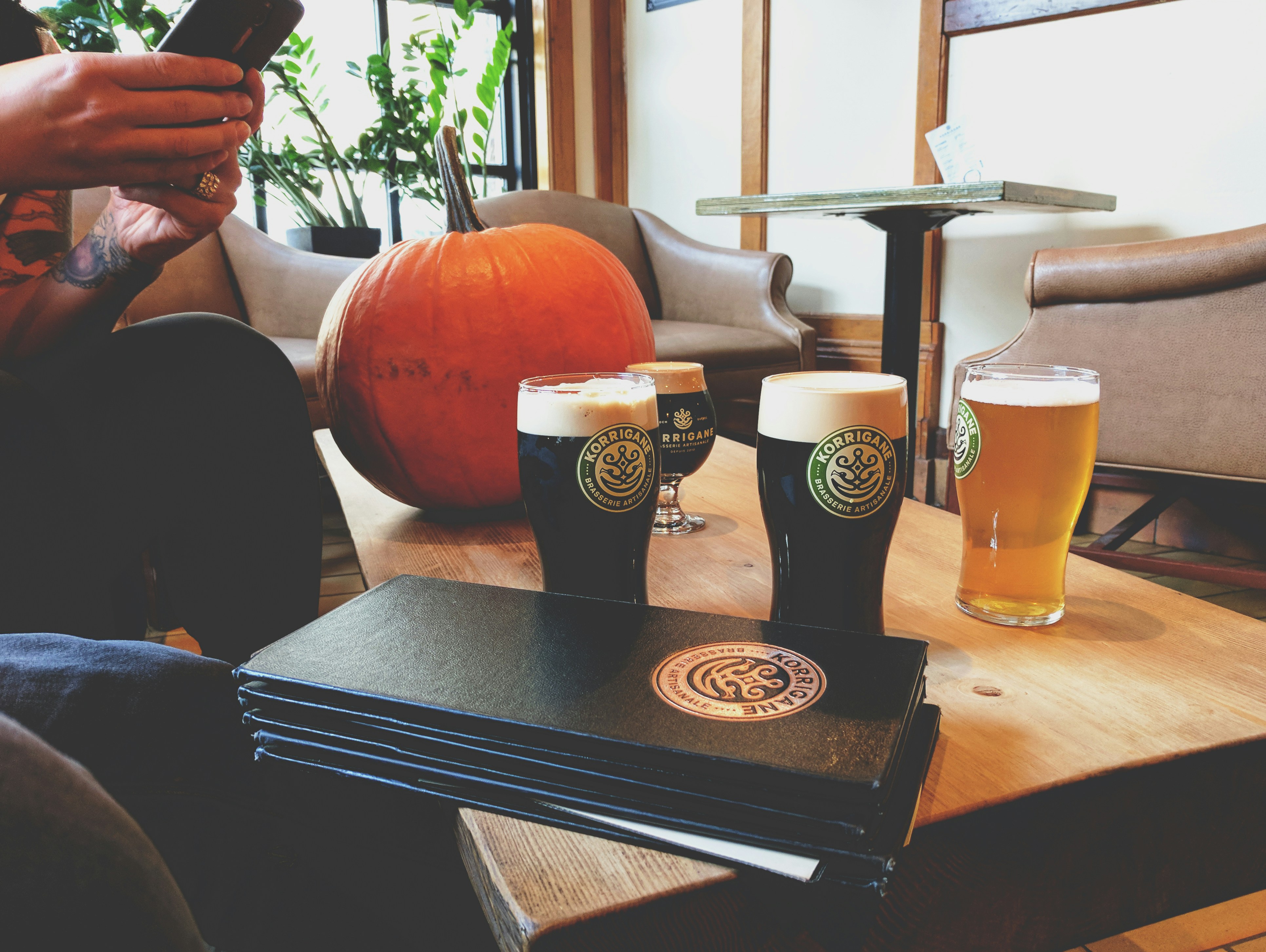 Cozy cafe table with three pints of stout and a large pumpkin centerpiece.