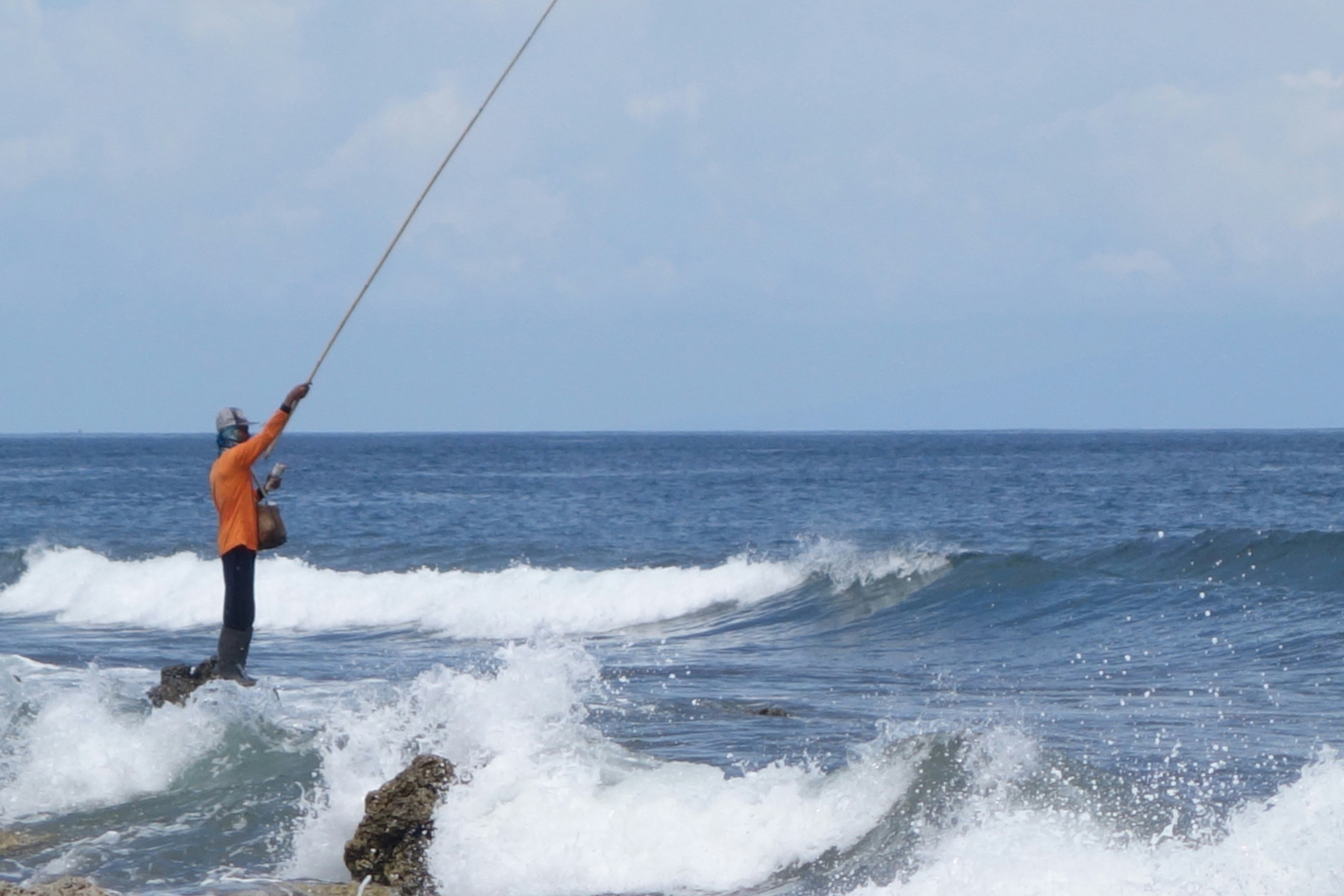 Lone surfer in orange shirt rides a breaking wave at sea