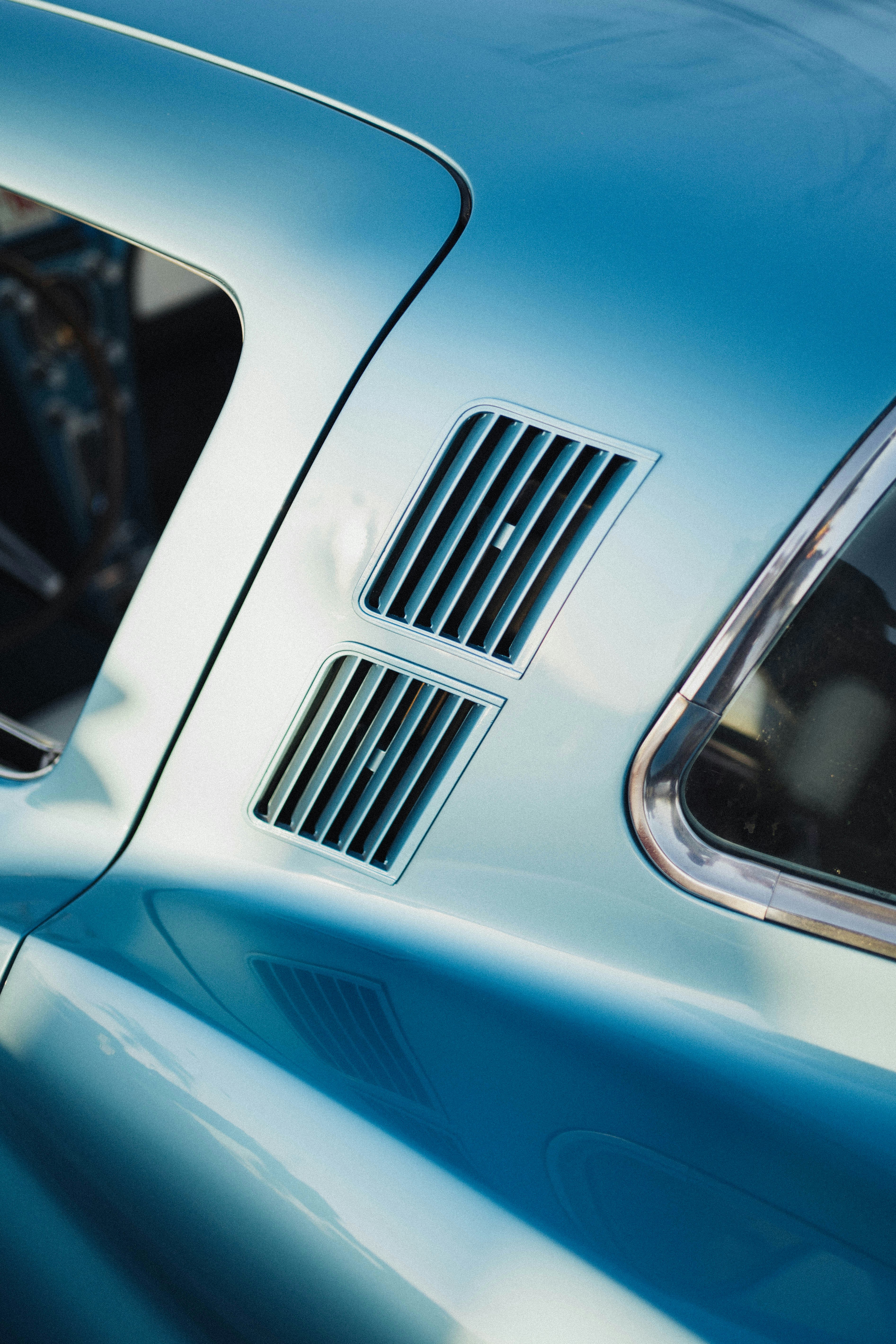Close-up of a vintage car's sleek blue body with distinctive air vents and a polished chrome trim.
