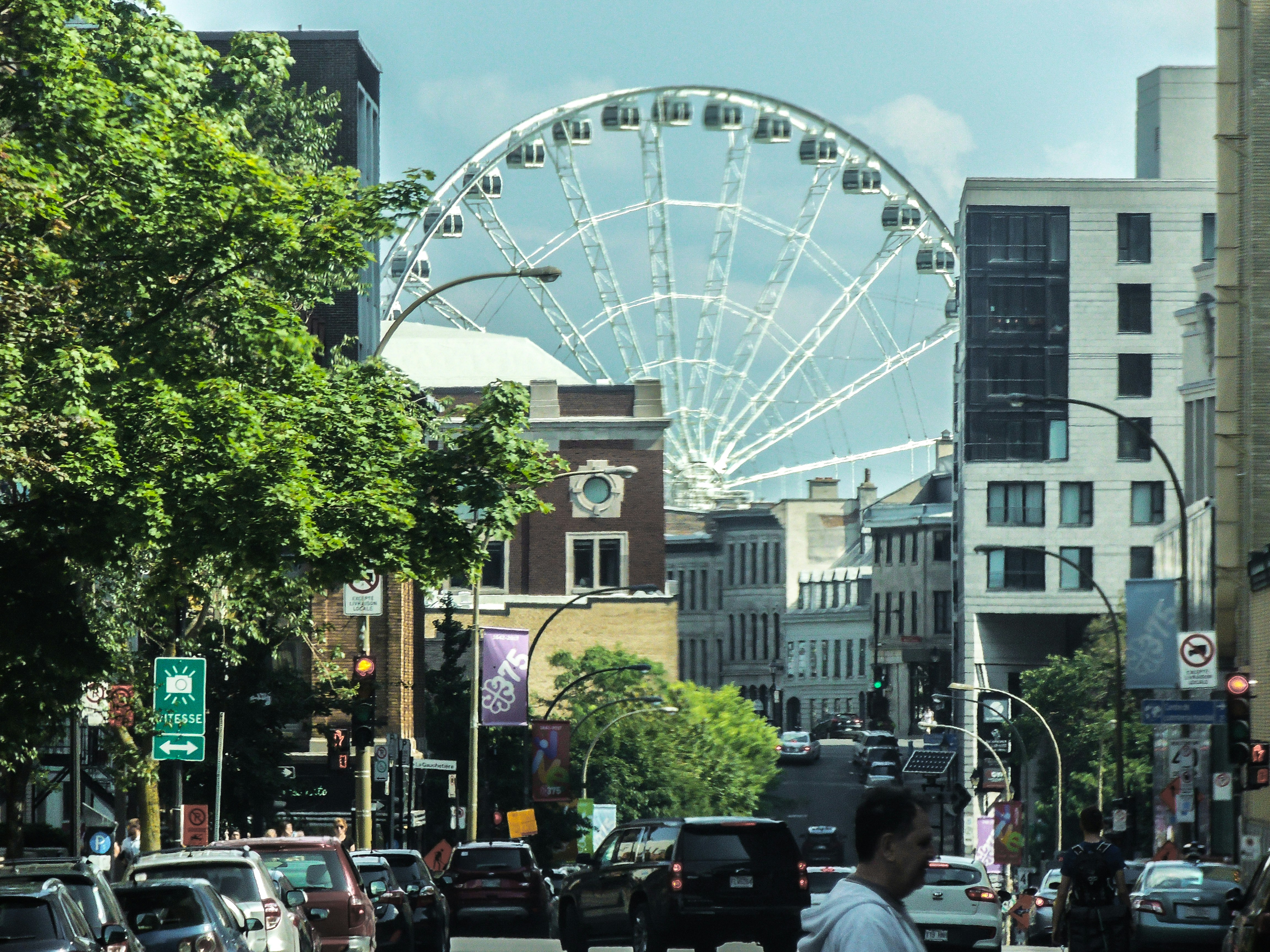 City street bustling with traffic, framed by a large ferris wheel in the background under a clear sky.