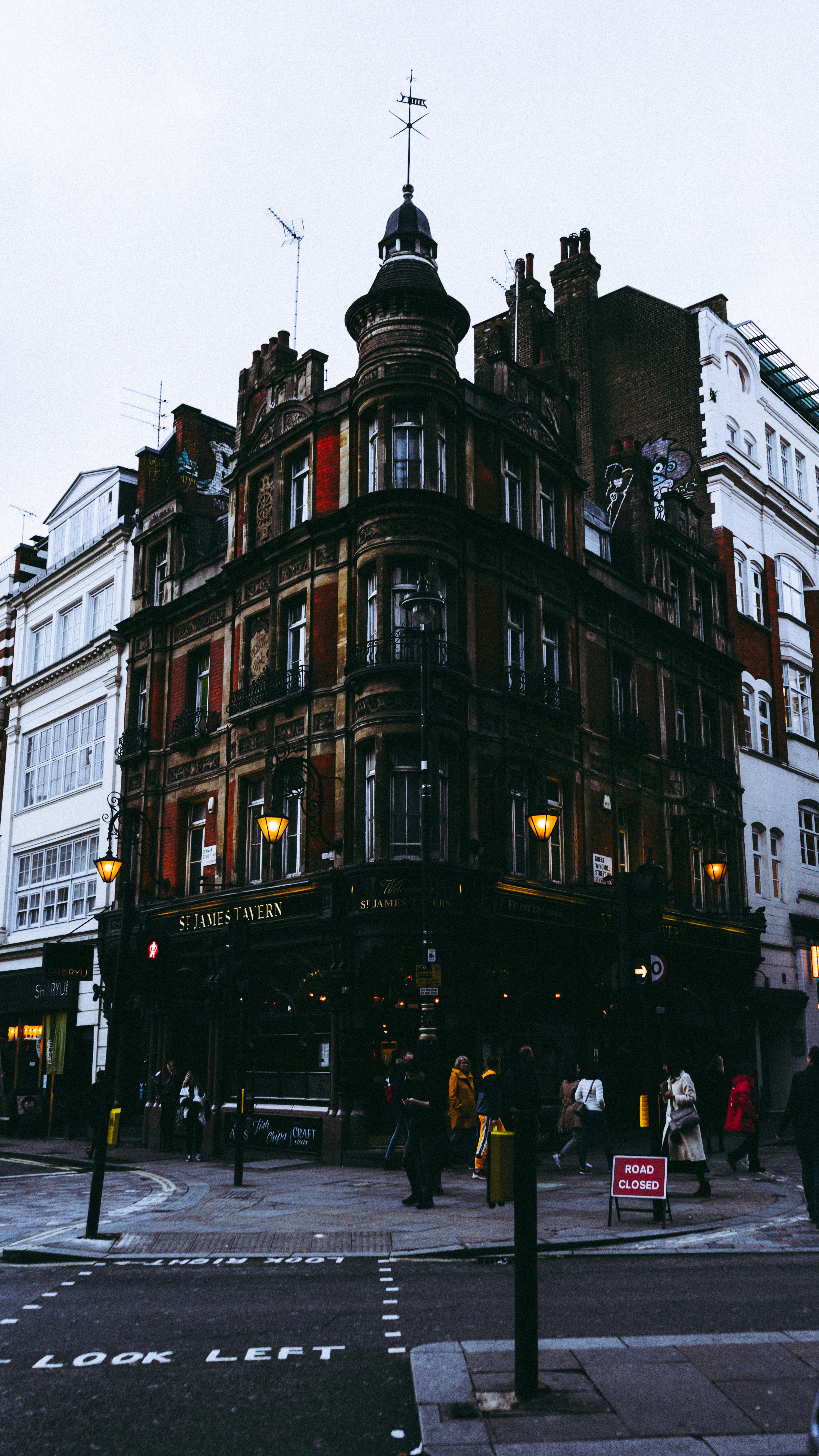 Historic pub facade featuring intricate architectural details, set against a bustling city backdrop. Warm streetlights illuminate the scene.