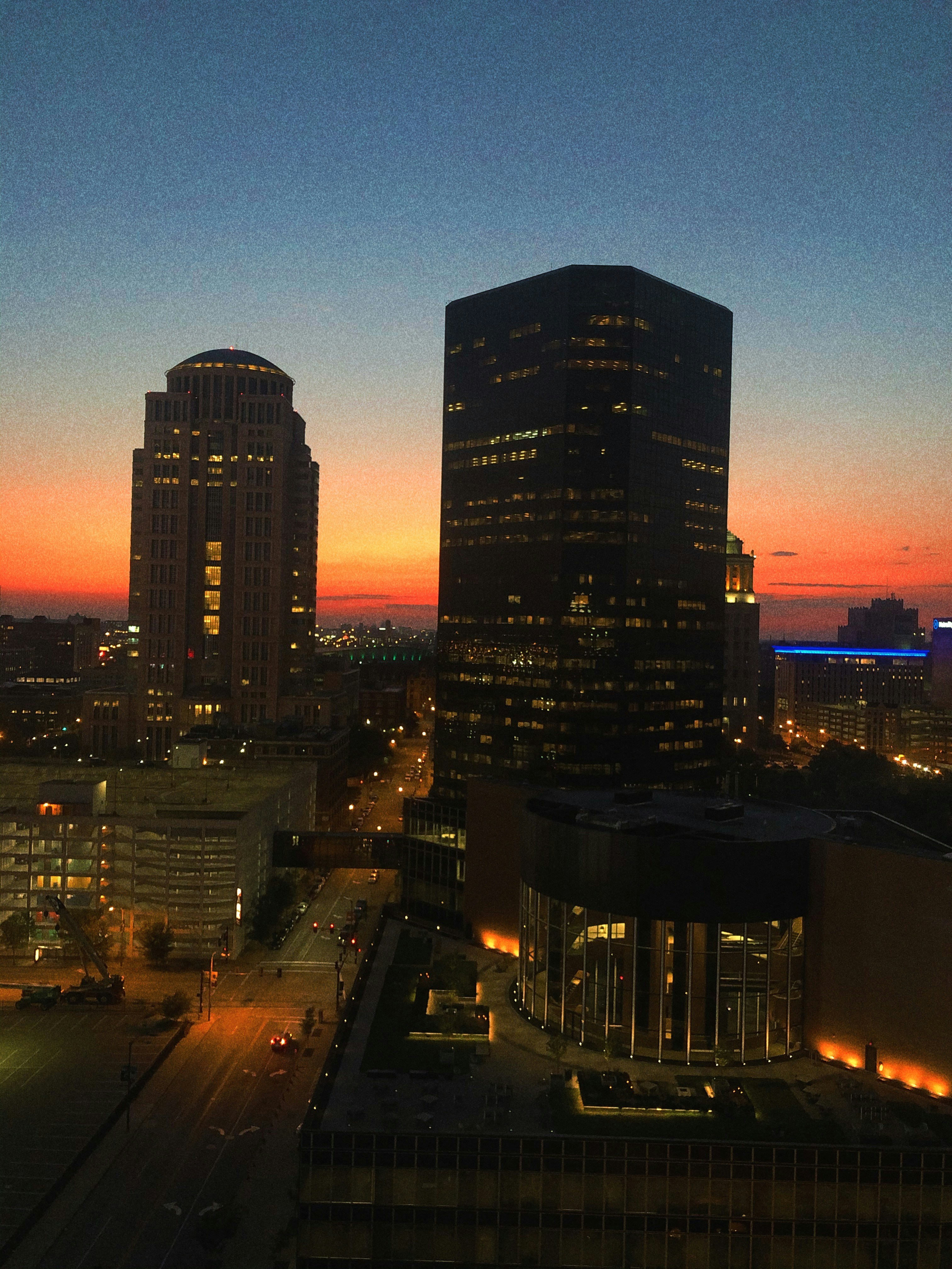 Silhouetted skyscrapers against a vibrant sunset, highlighting the transition from day to night in an urban landscape.