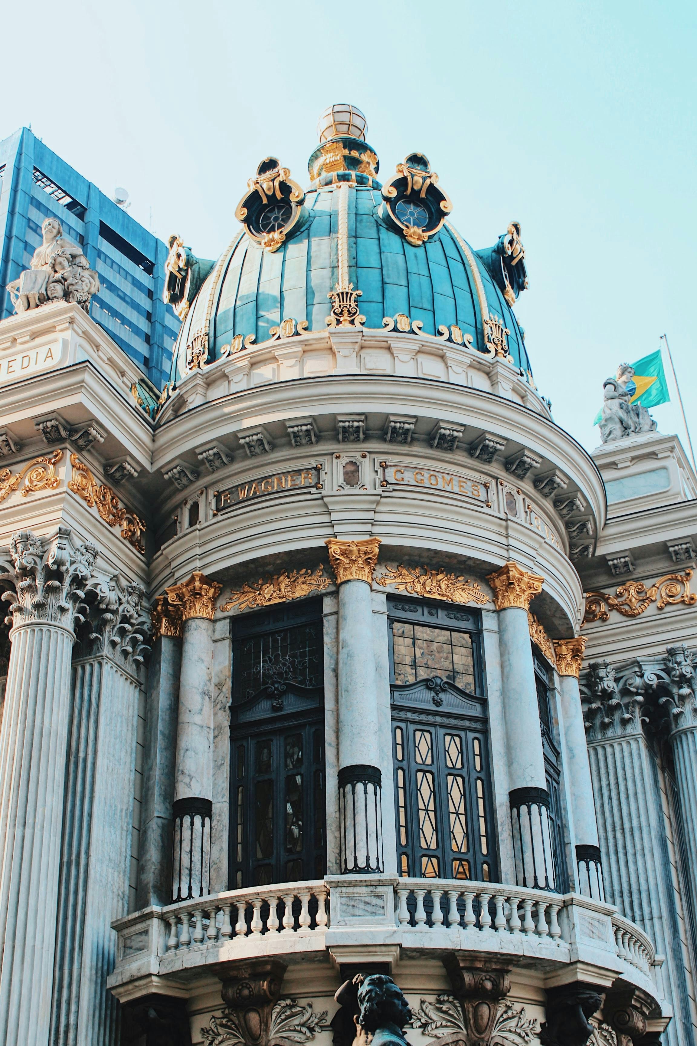 Ornate building facade with a turquoise dome and intricate columns against a bright blue sky.