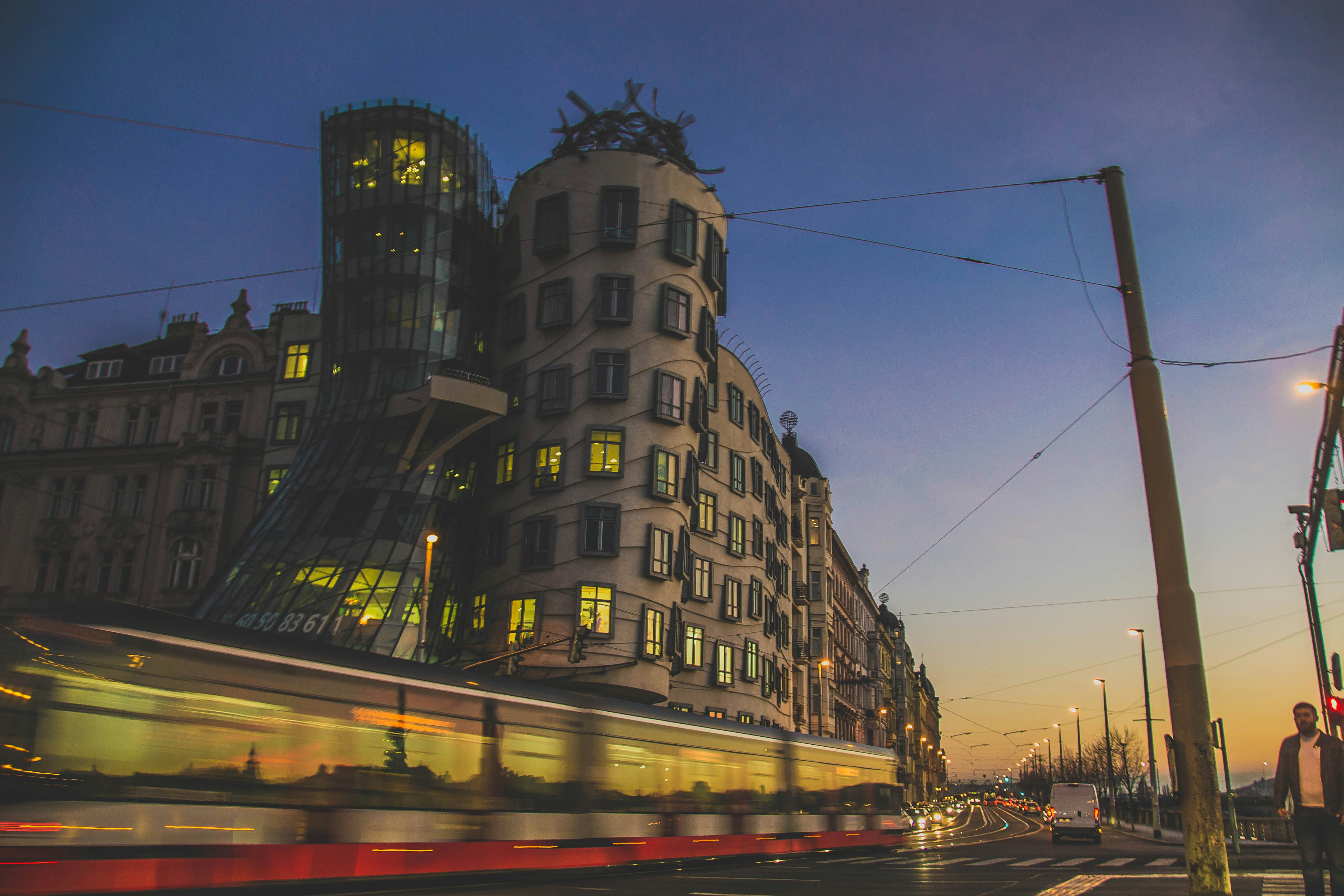 Dusk Over the Dancing House: A Tram's Blur Across a Curved City Façade