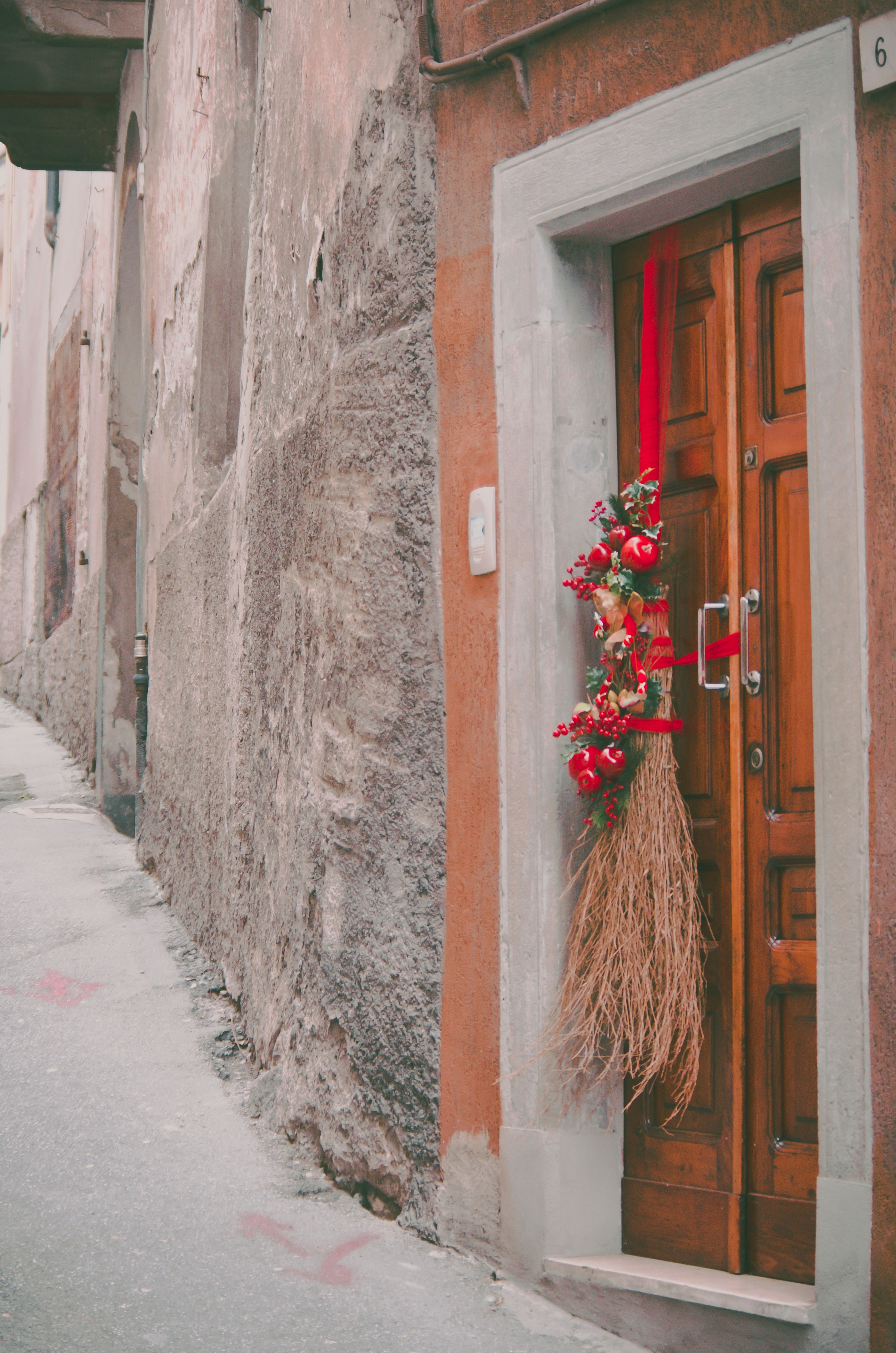 Wooden door decorated with a festive wreath and ribbons, set against a textured stone wall in a narrow alleyway.