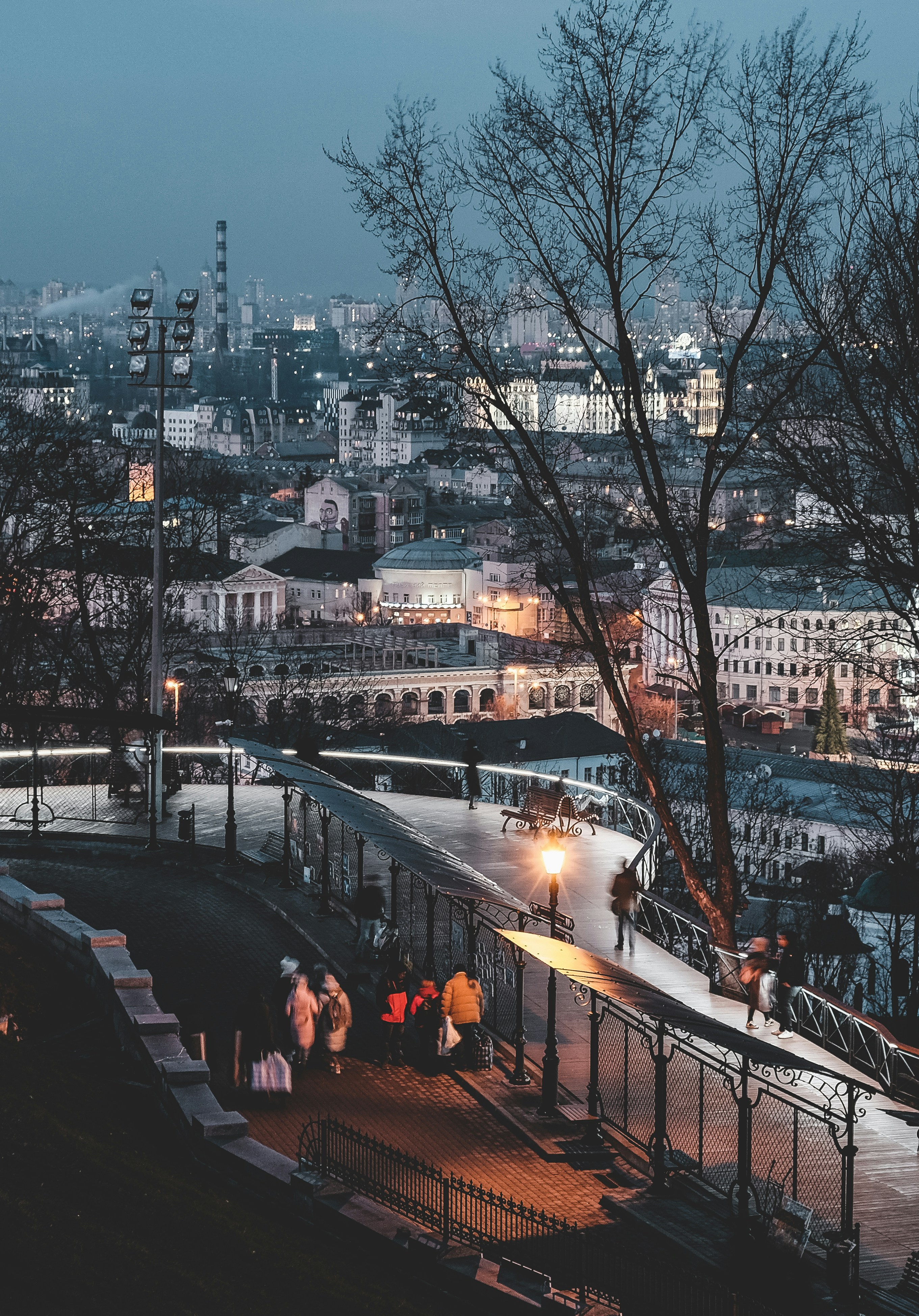 Dusk Along a Riverside Promenade: City Lights Framed by Bare Branches