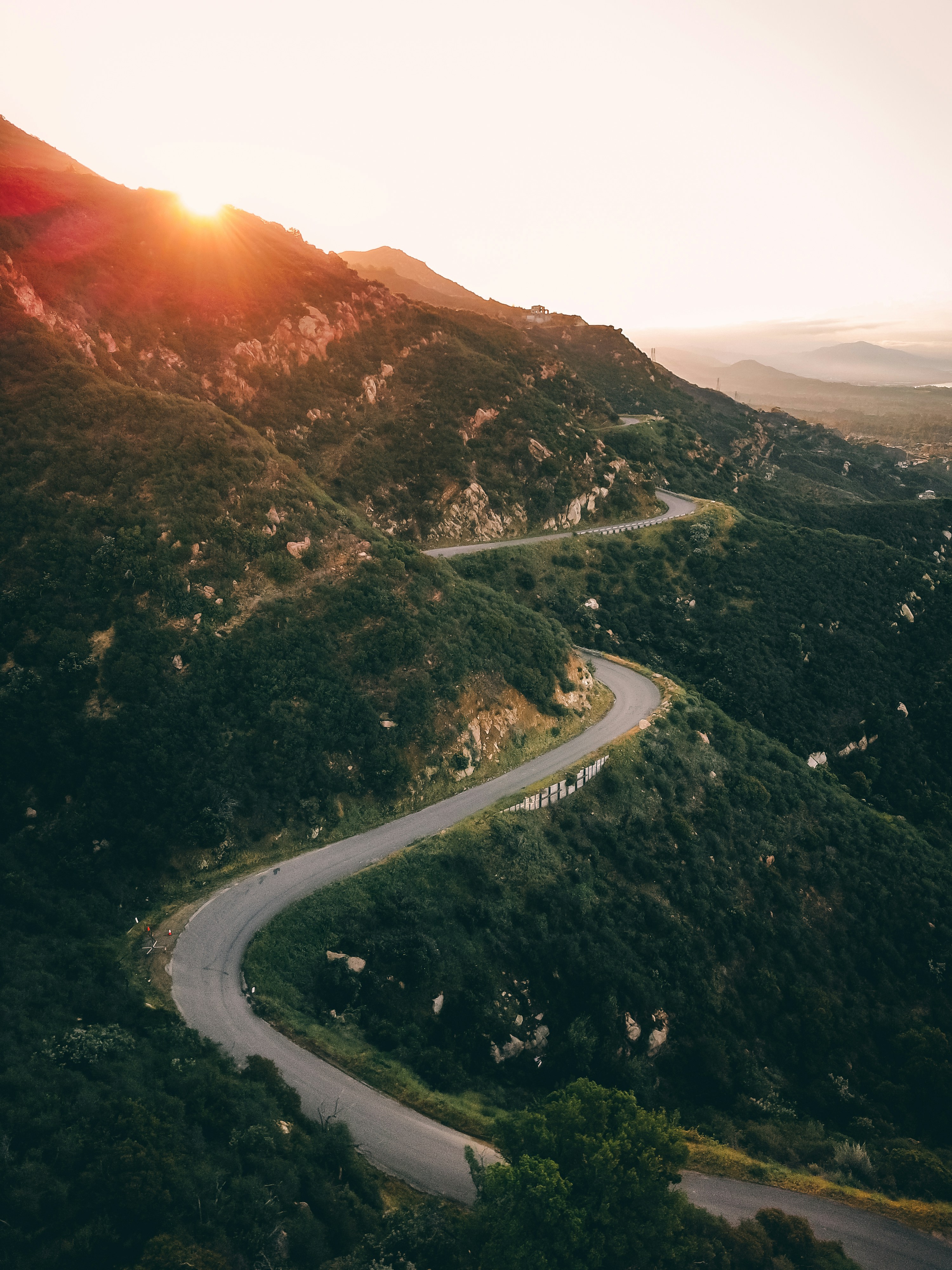 Curved road meanders through lush green hills under a warm sunset glow.