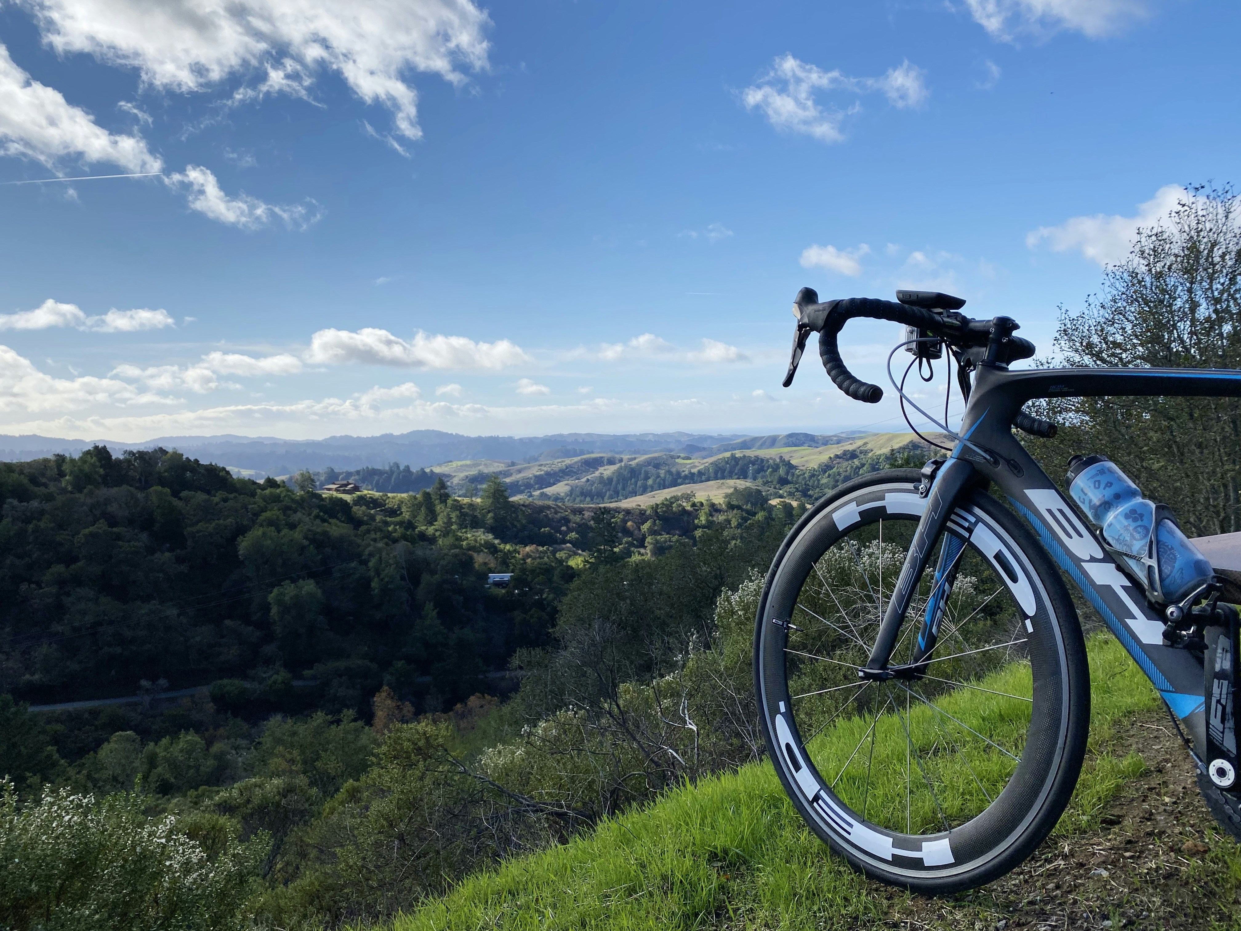 Road bike positioned on grassy hill overlooking expansive valley under a partly cloudy sky.