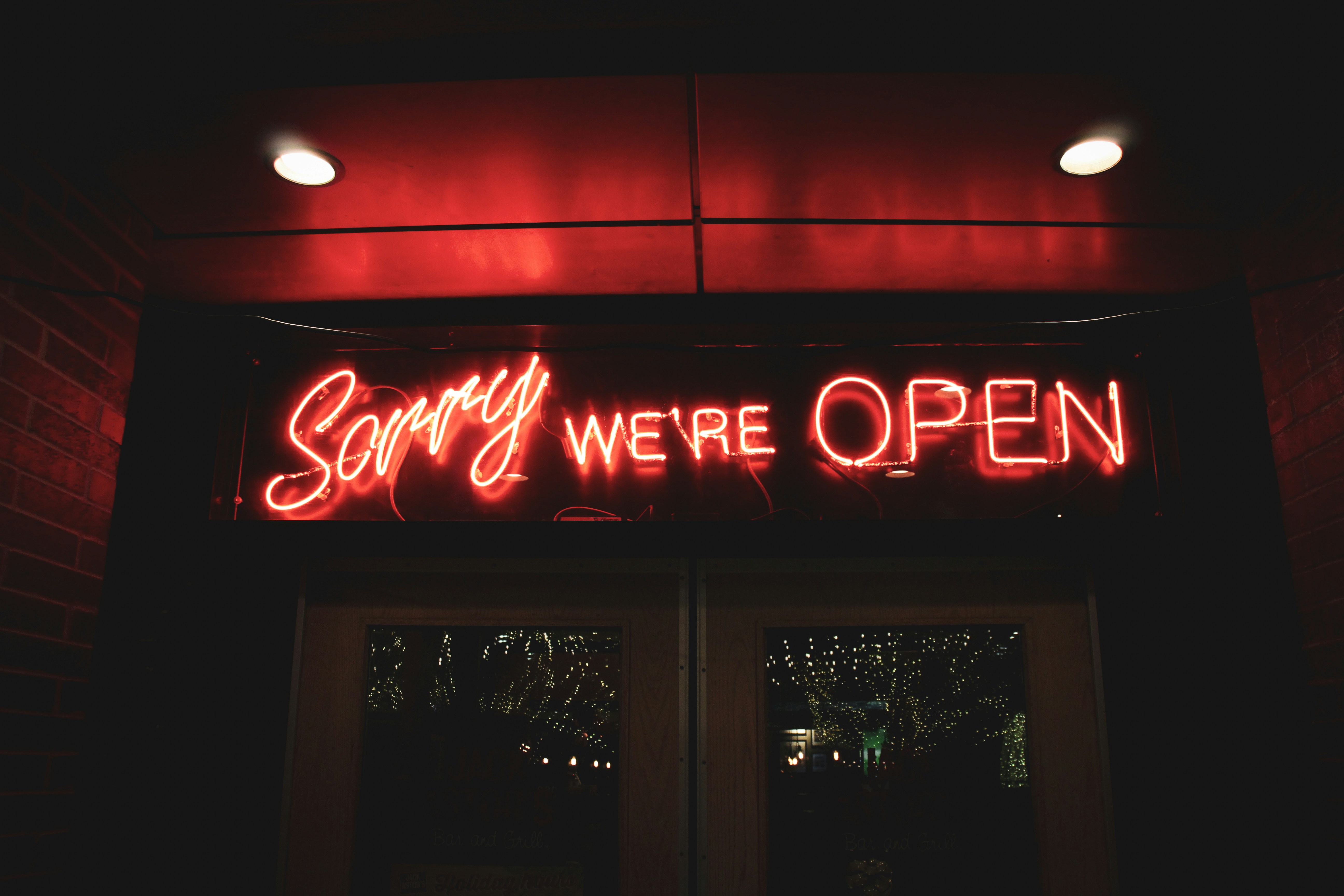 Red neon sign reading 'Sorry We're Open' against a dark background.