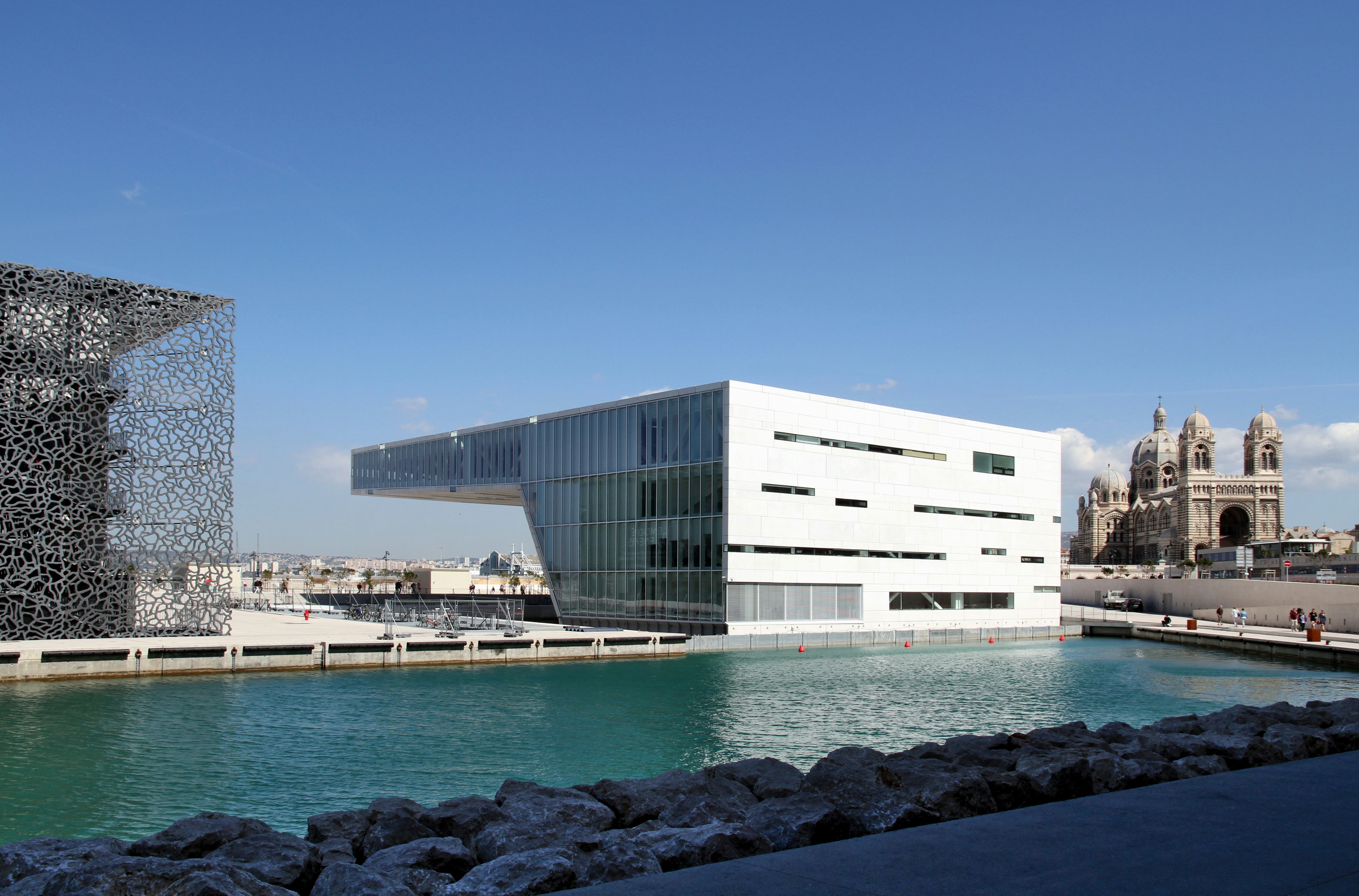 Contemporary white building beside a calm harbor under a clear blue sky.