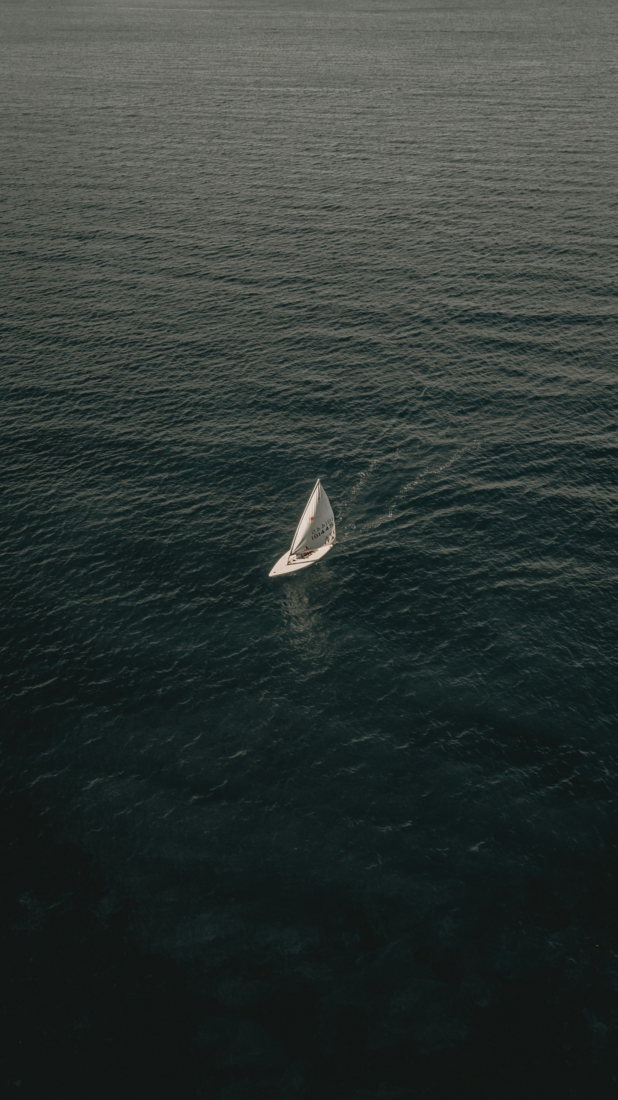 Lone Sailboat Tracing a Quiet Sea from the Sky