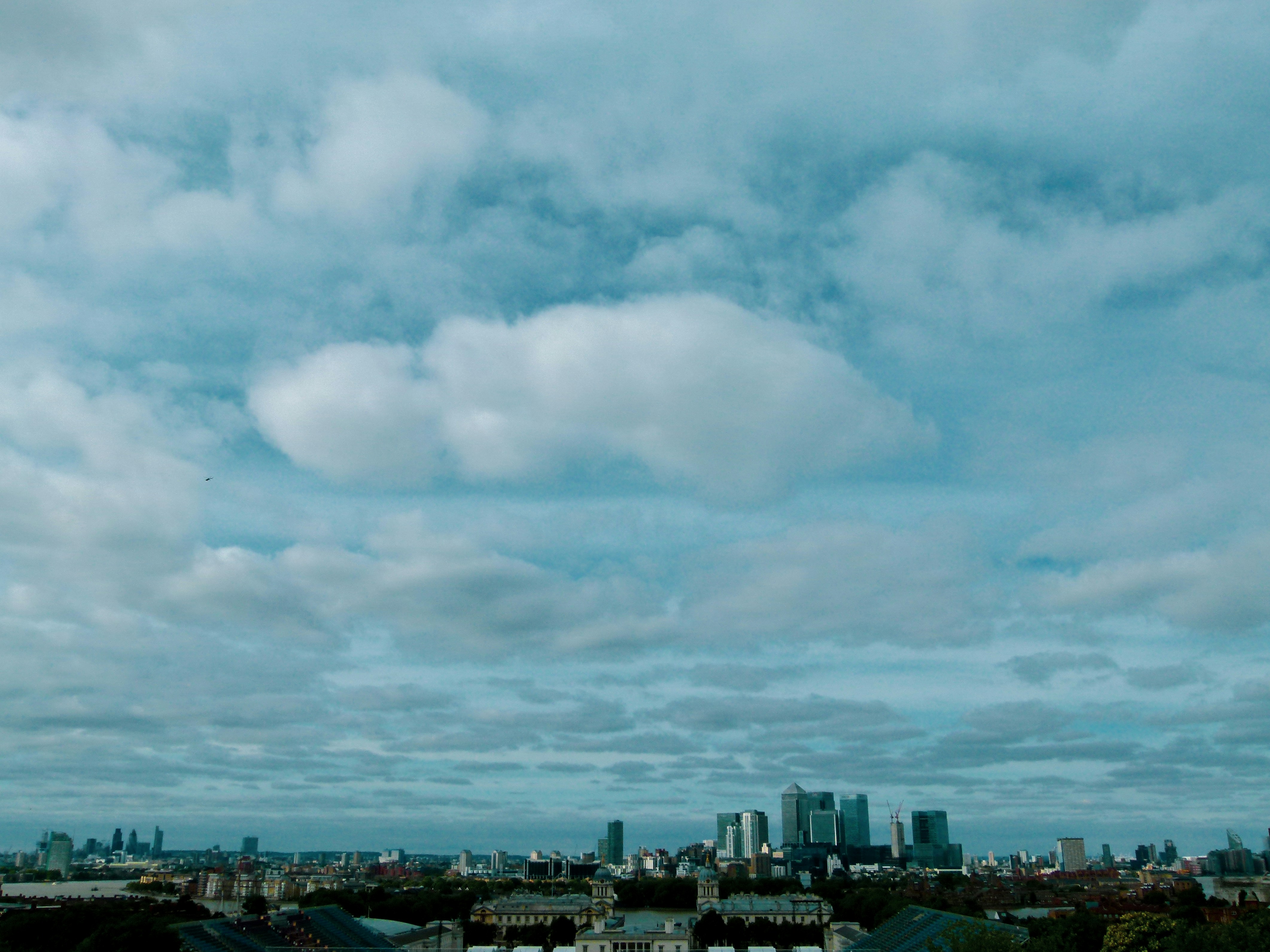 A panoramic view of a city skyline framed by a soft, cloudy sky, showcasing a blend of modern architecture and nature below.