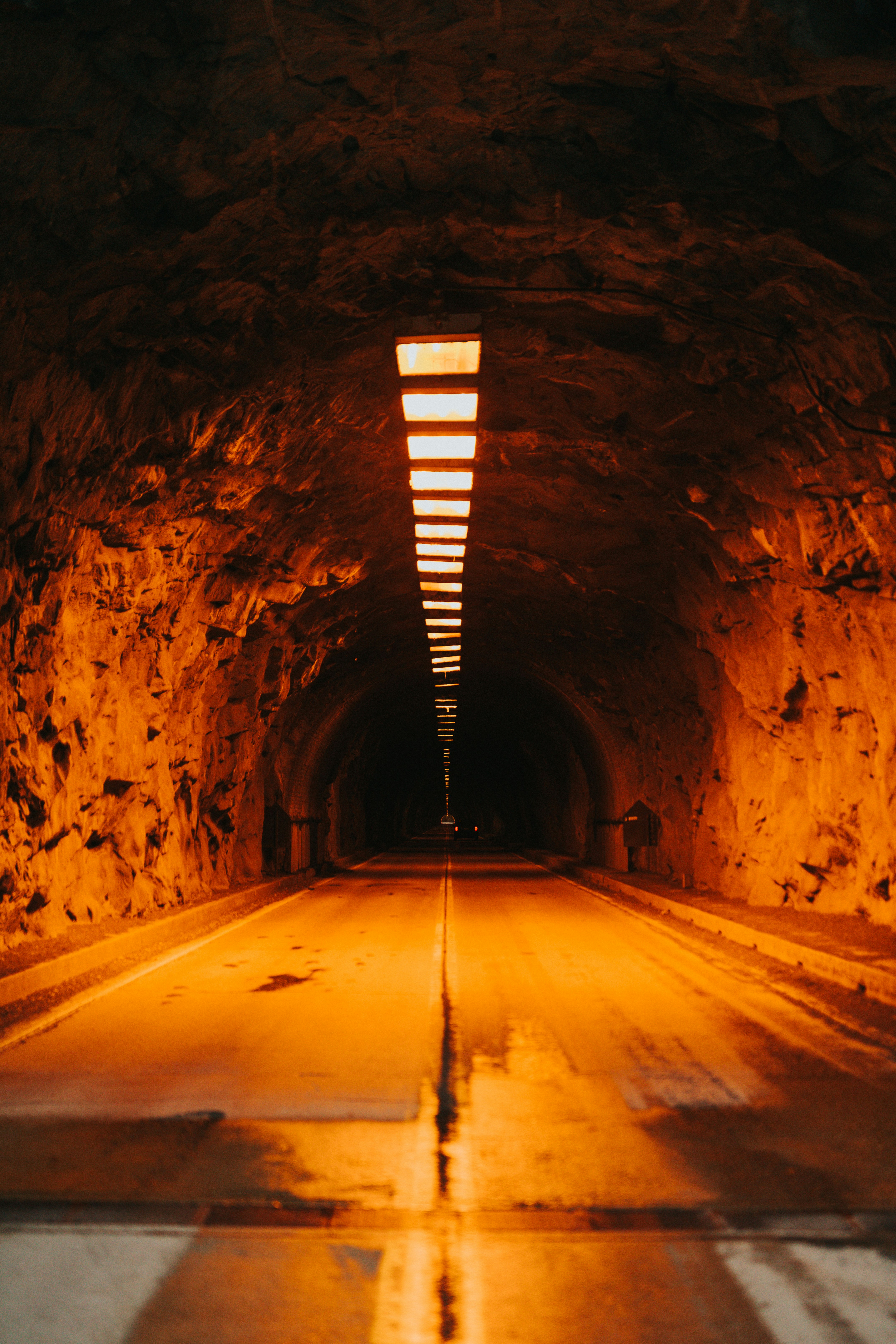 A dimly lit tunnel with glistening wet pavement and warm orange lighting reflecting off the rocky walls.