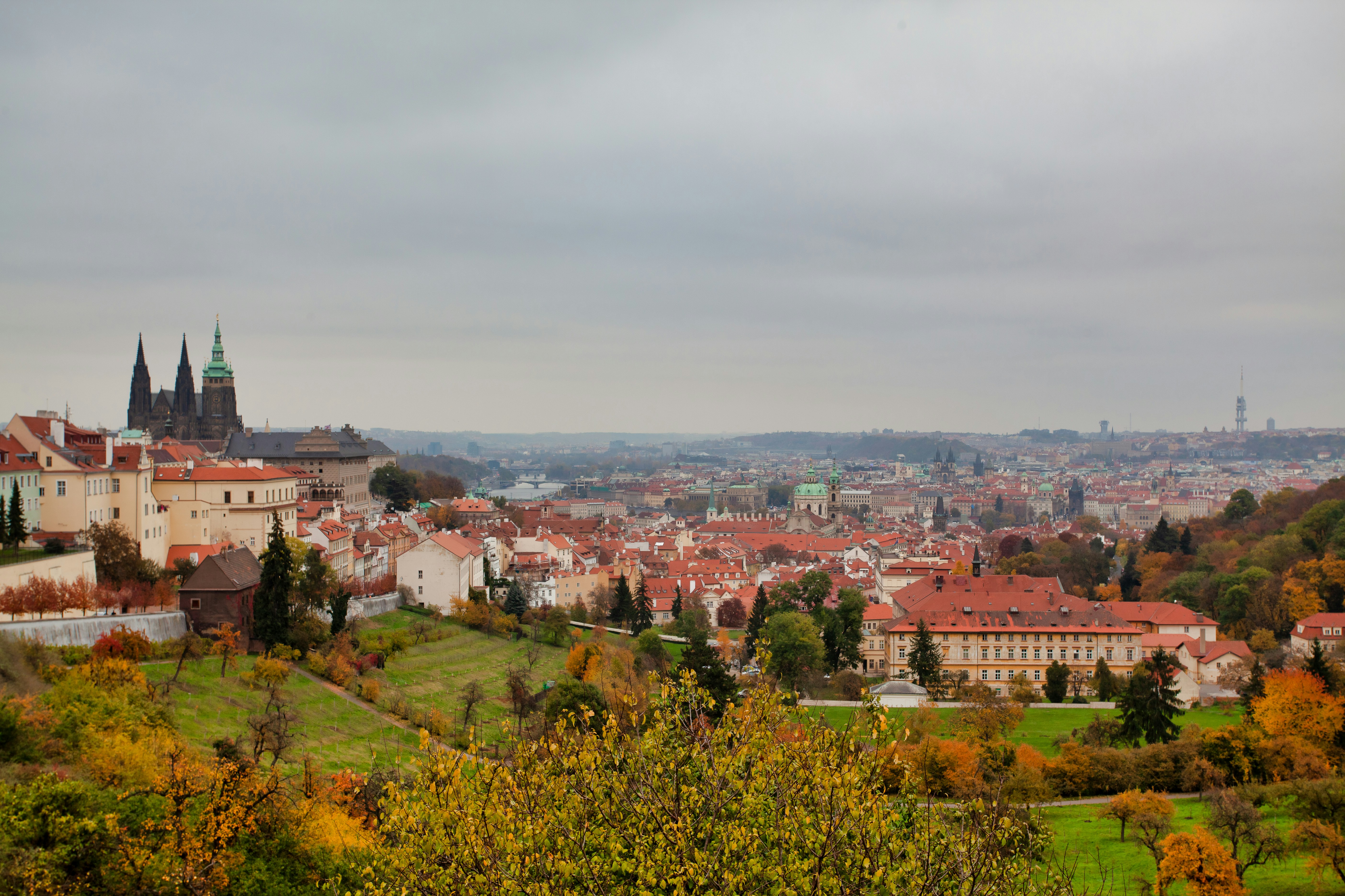 View of a historic cityscape with red rooftops and distant spires under an overcast sky.