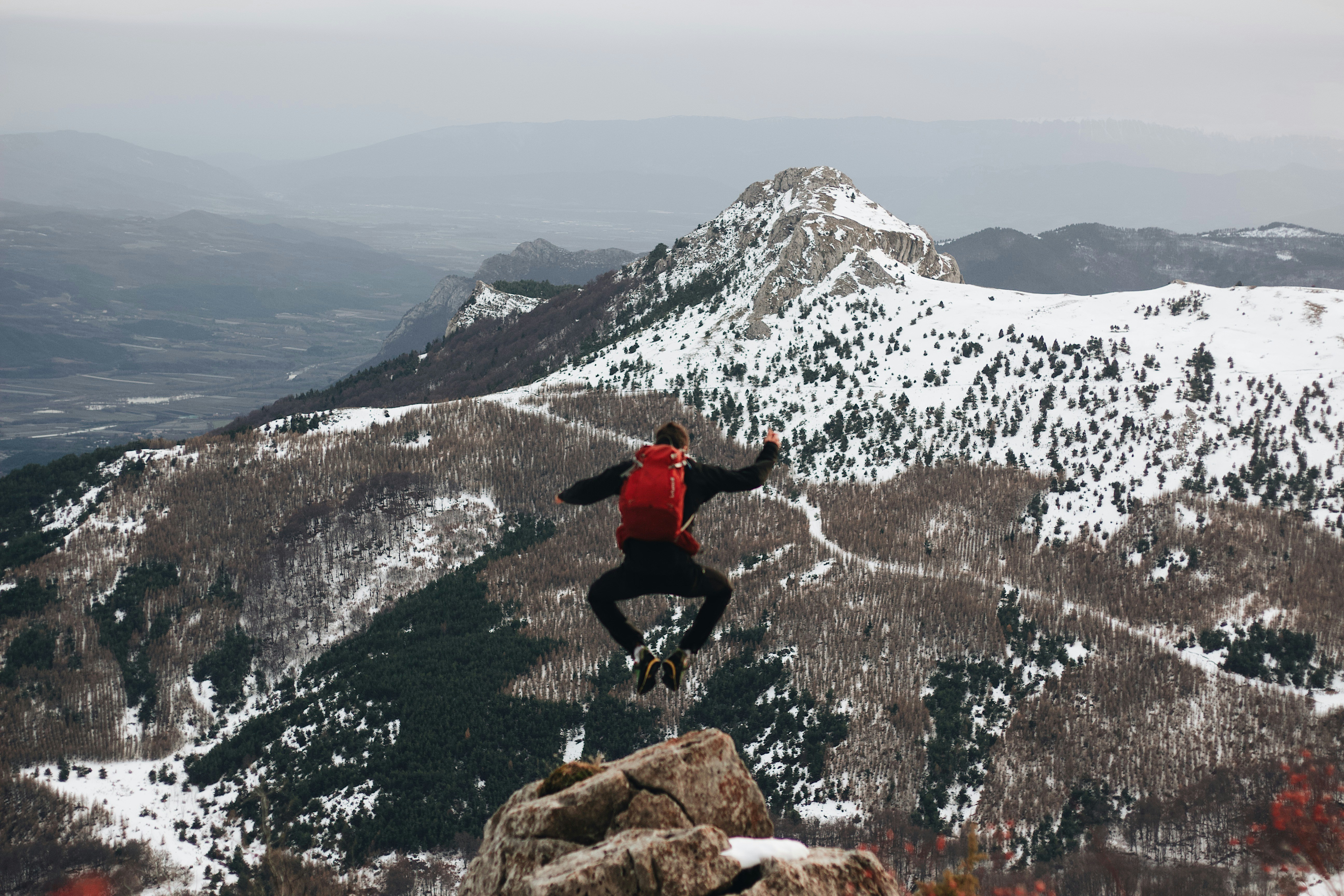 Homme sautant sur un rocher face à des montagnes avec de la neige photo ...