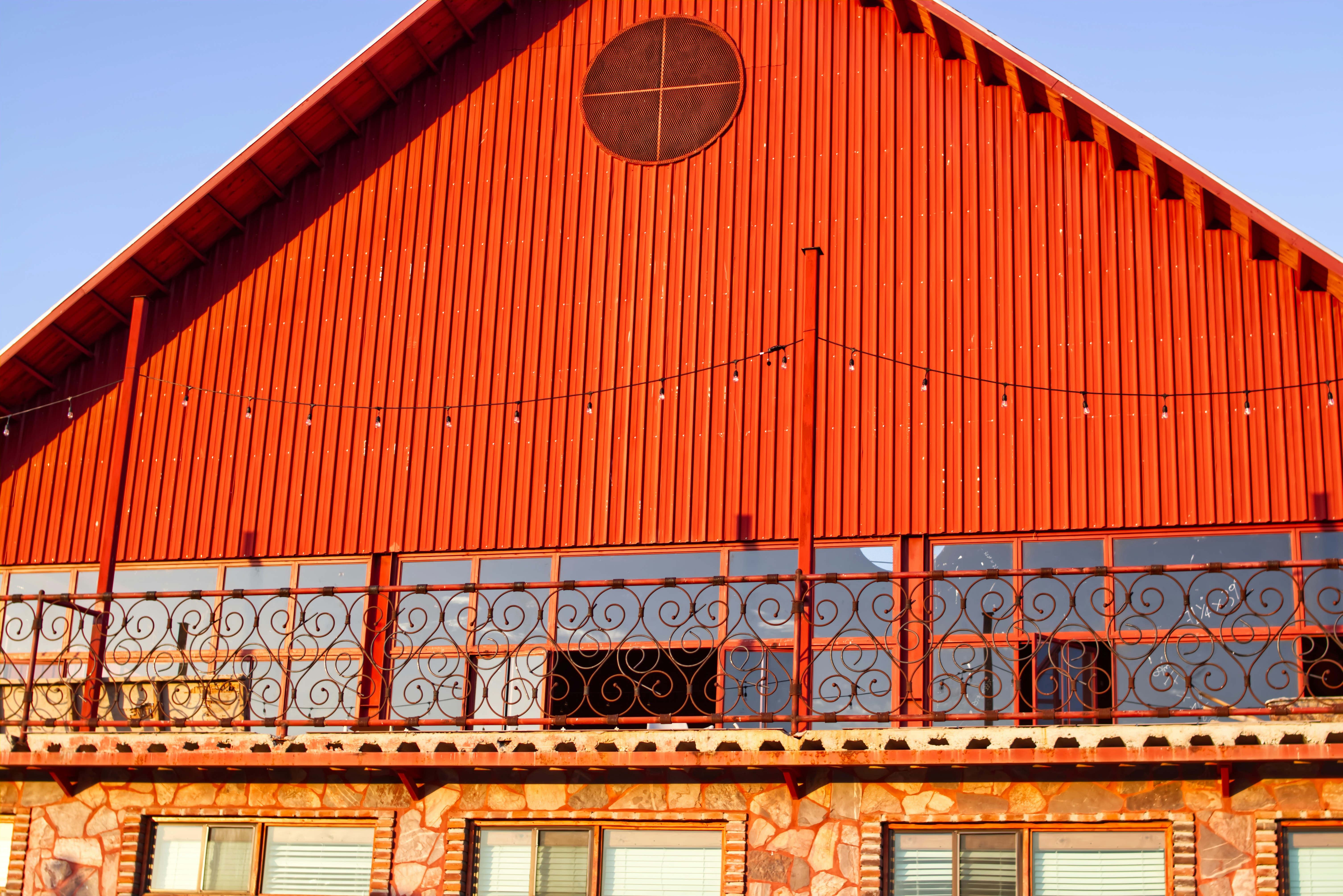 Red barn with intricate wrought iron balcony railing under a clear blue sky.