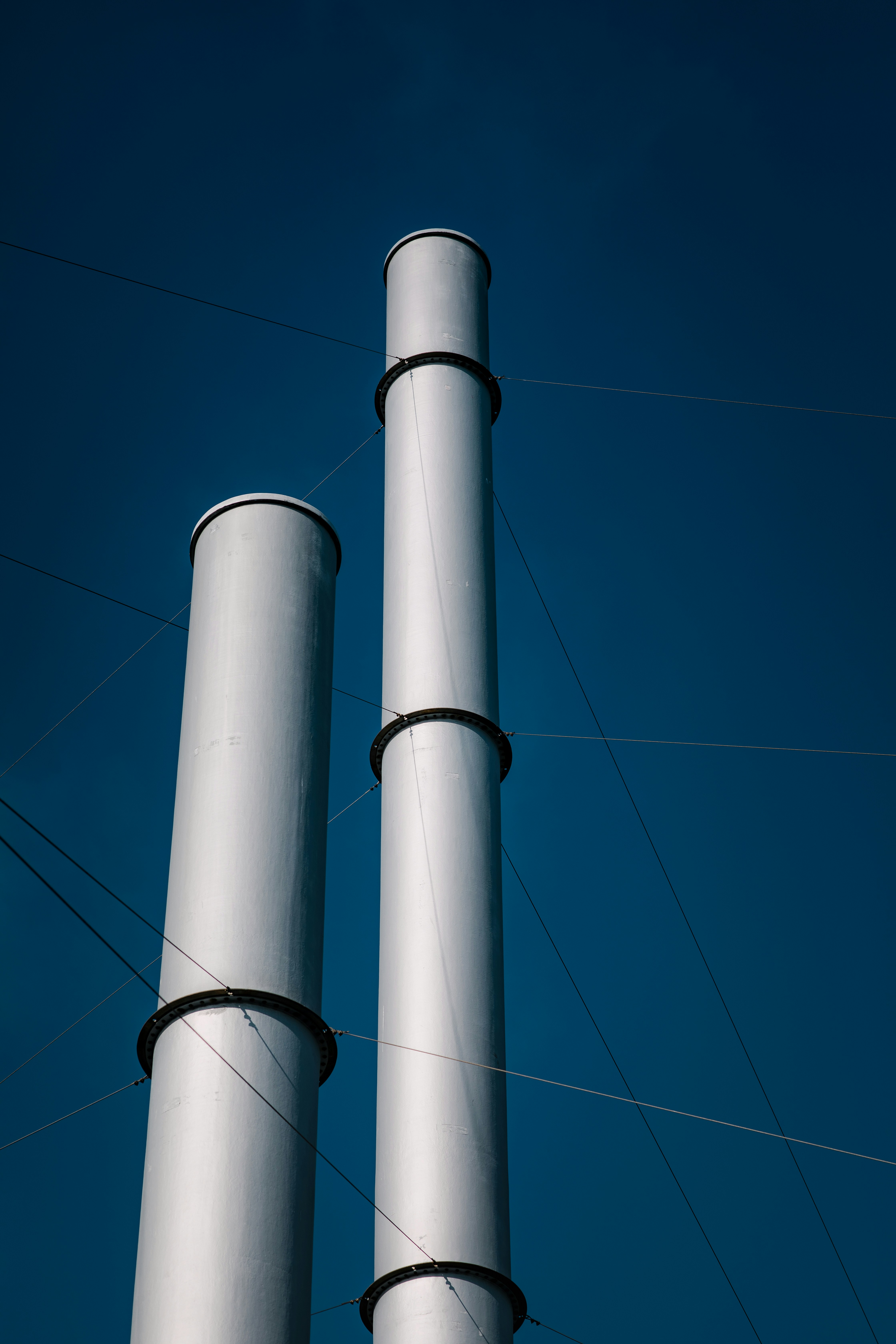 Two towering smokestacks rise against a clear blue sky, framed by intersecting power lines.