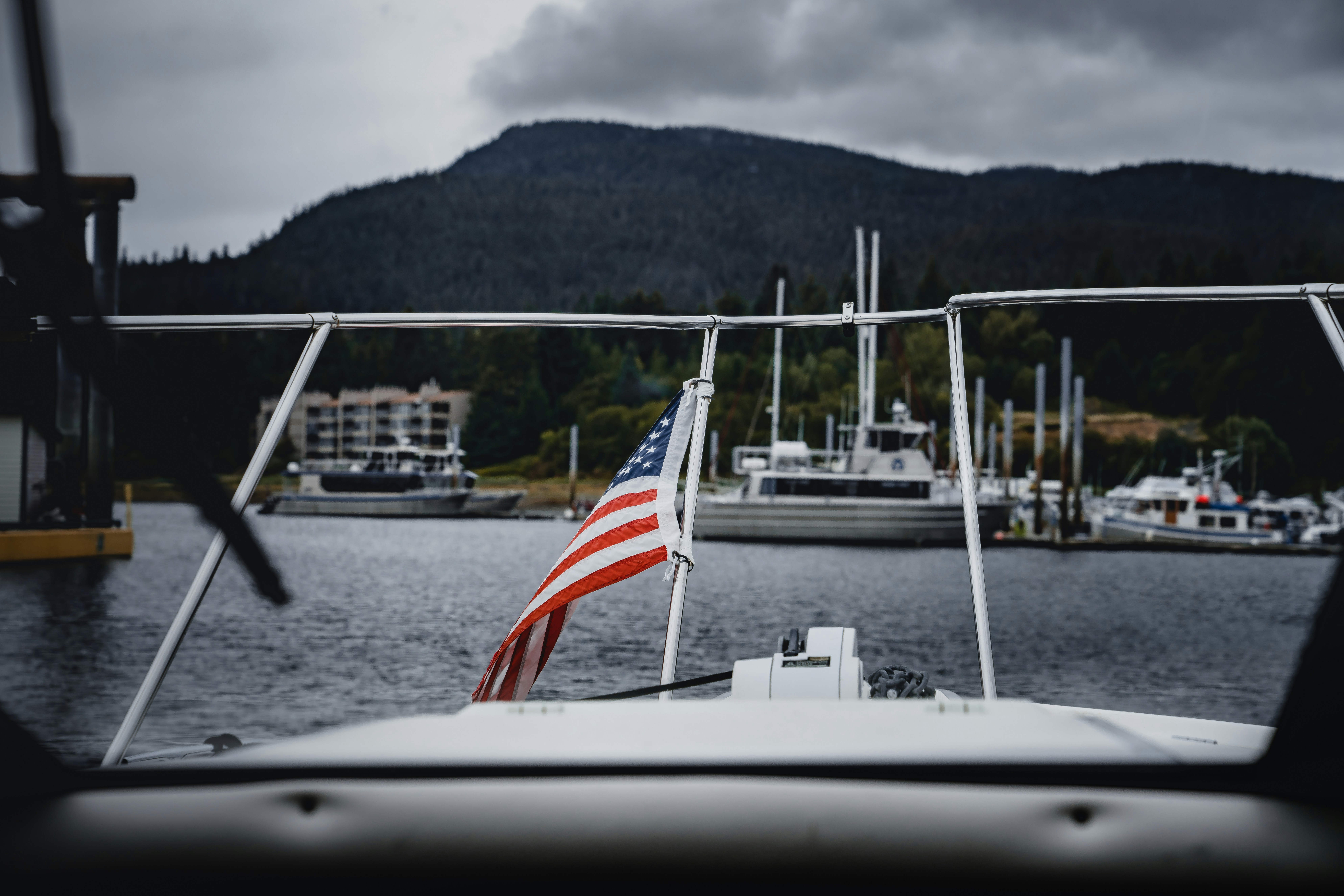 Flag on the Bow: Harbor Boats Framed by Misty Mountain Backdrop