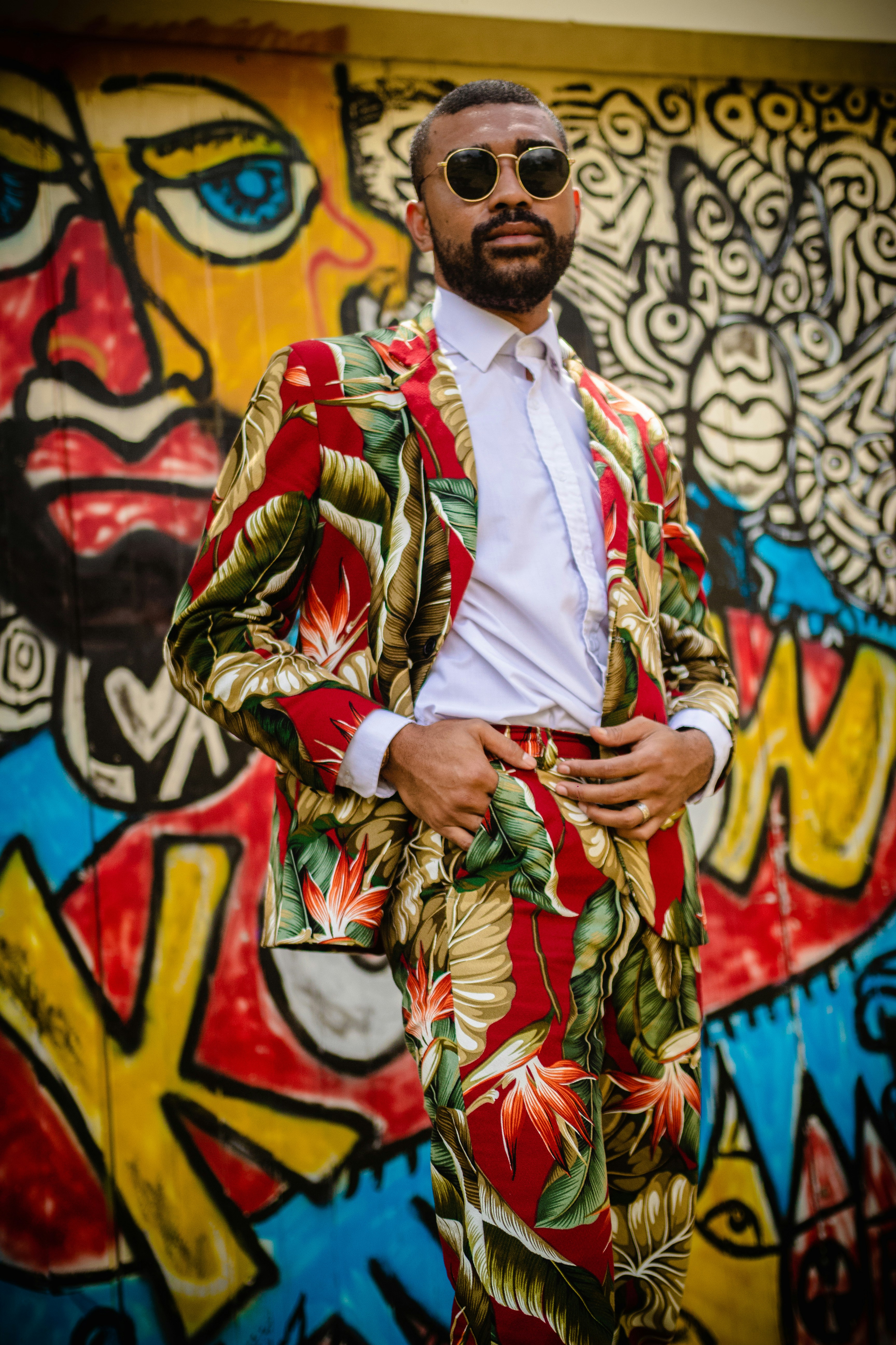A man in a bold floral suit poses confidently against a colorful mural, showcasing a blend of contemporary fashion and urban art.