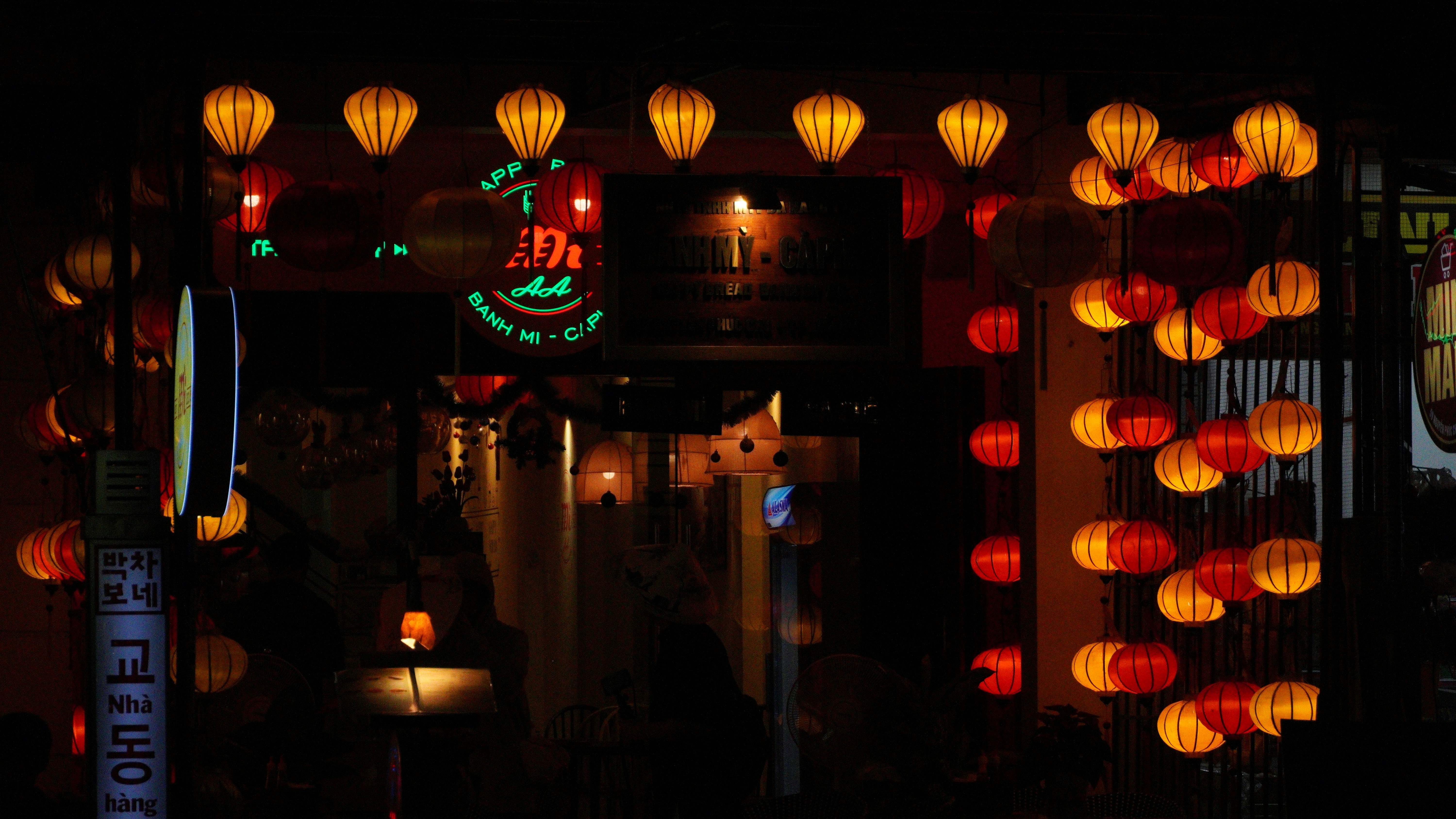 Vibrant paper lanterns illuminate a cozy street café in Hoi An, casting warm hues against the night.