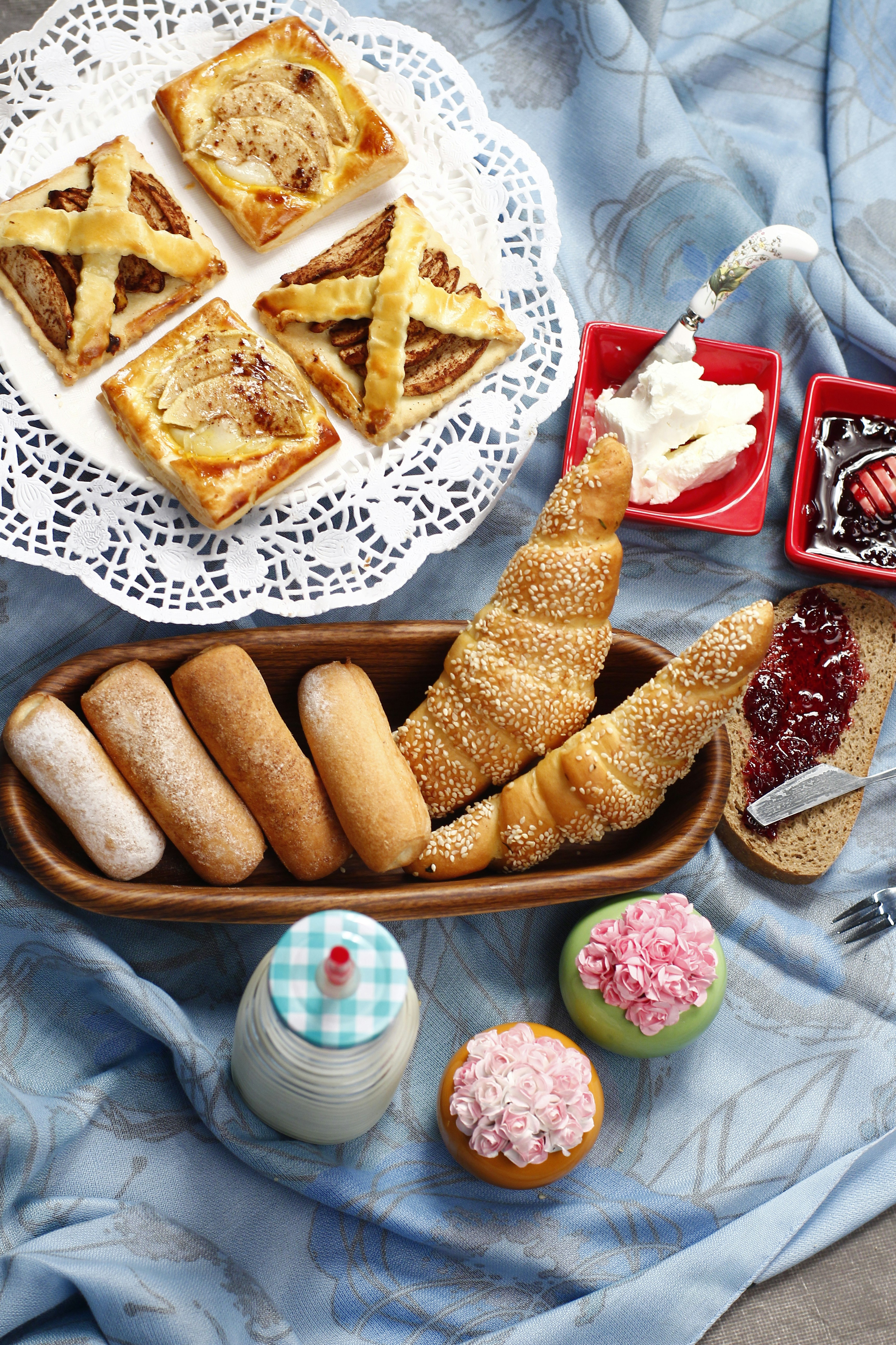 An inviting assortment of pastries, including fruit tarts and croissants, arranged on a decorative tablecloth with colorful accompaniments. Perfect for a cozy breakfast setting.