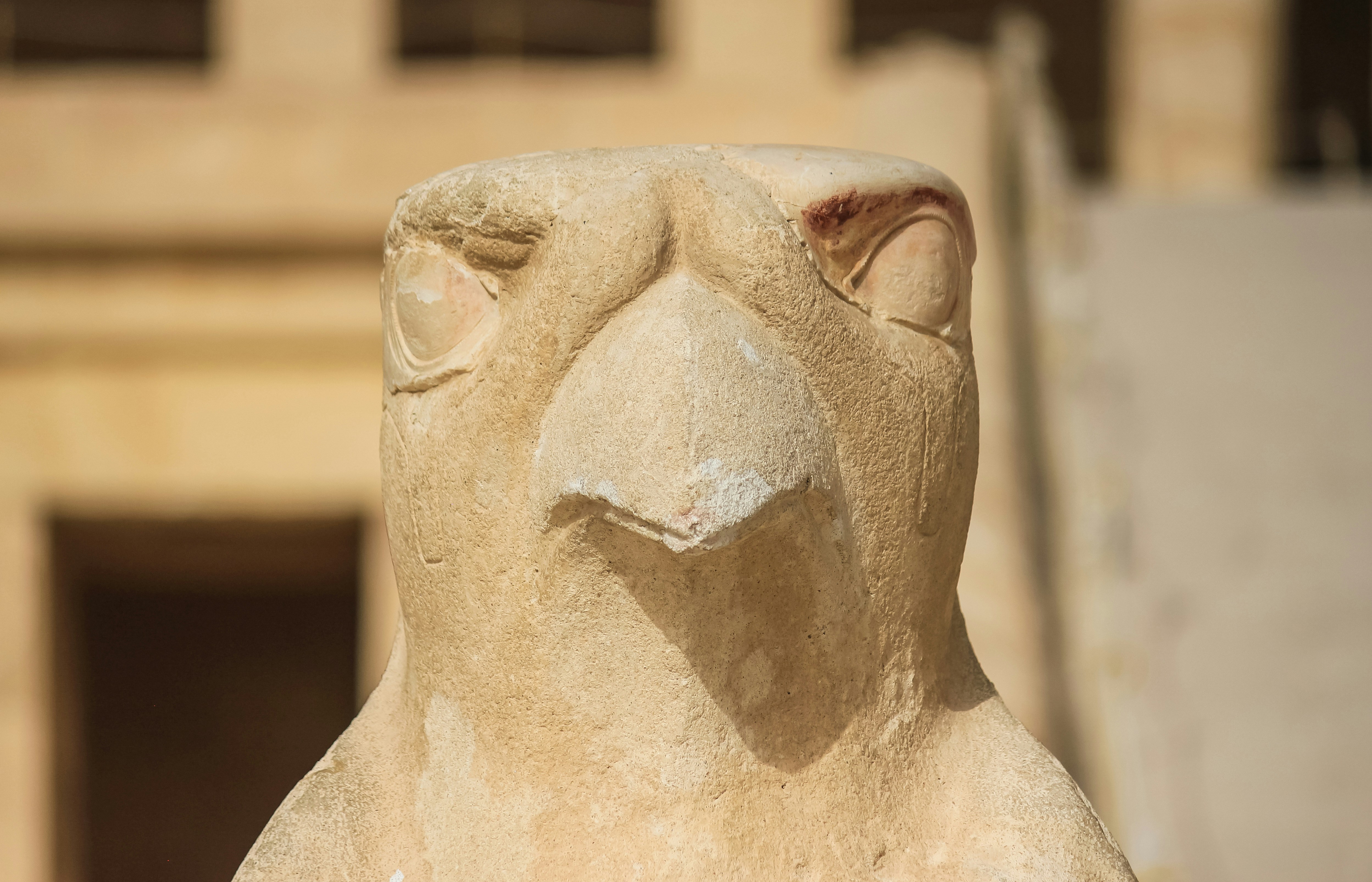 Weathered sculpture of a falcon, symbolizing strength and protection, stands against a backdrop of ancient architecture.