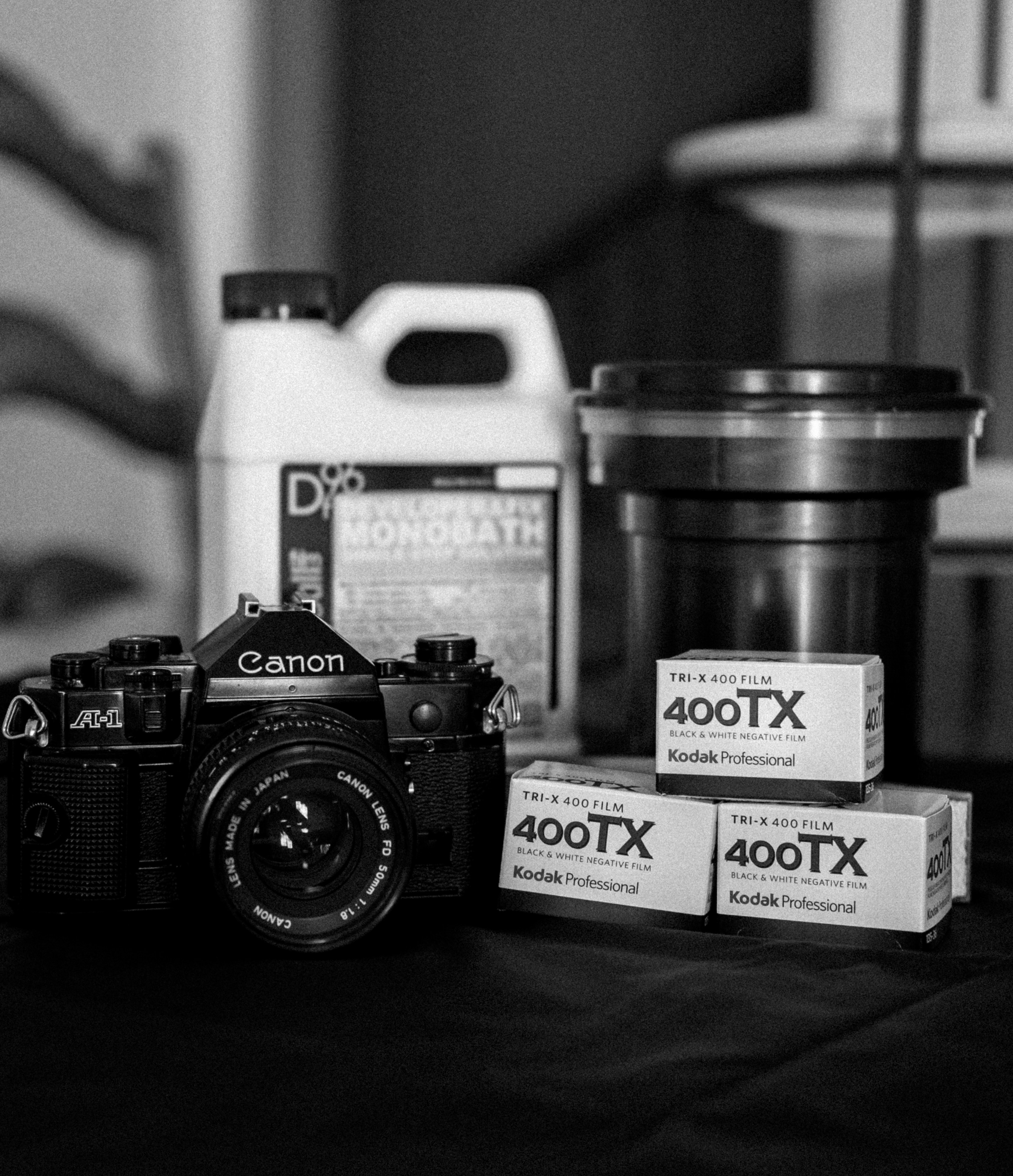 Canon A-1 camera with Kodak 400TX film and developing supplies arranged on a black surface.
