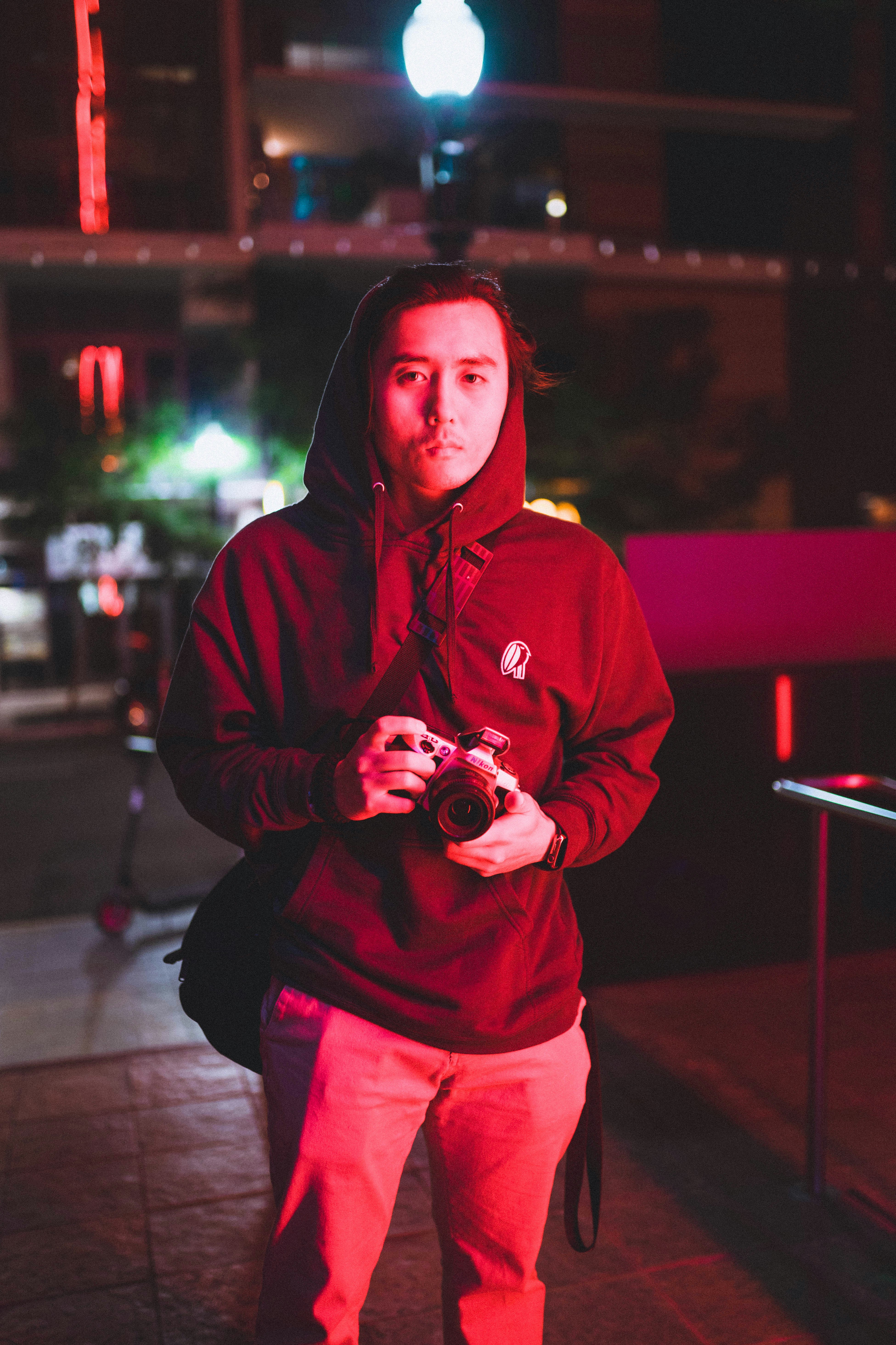 Neon Night Portrait: Hooded Photographer with a Camera in the City Glow