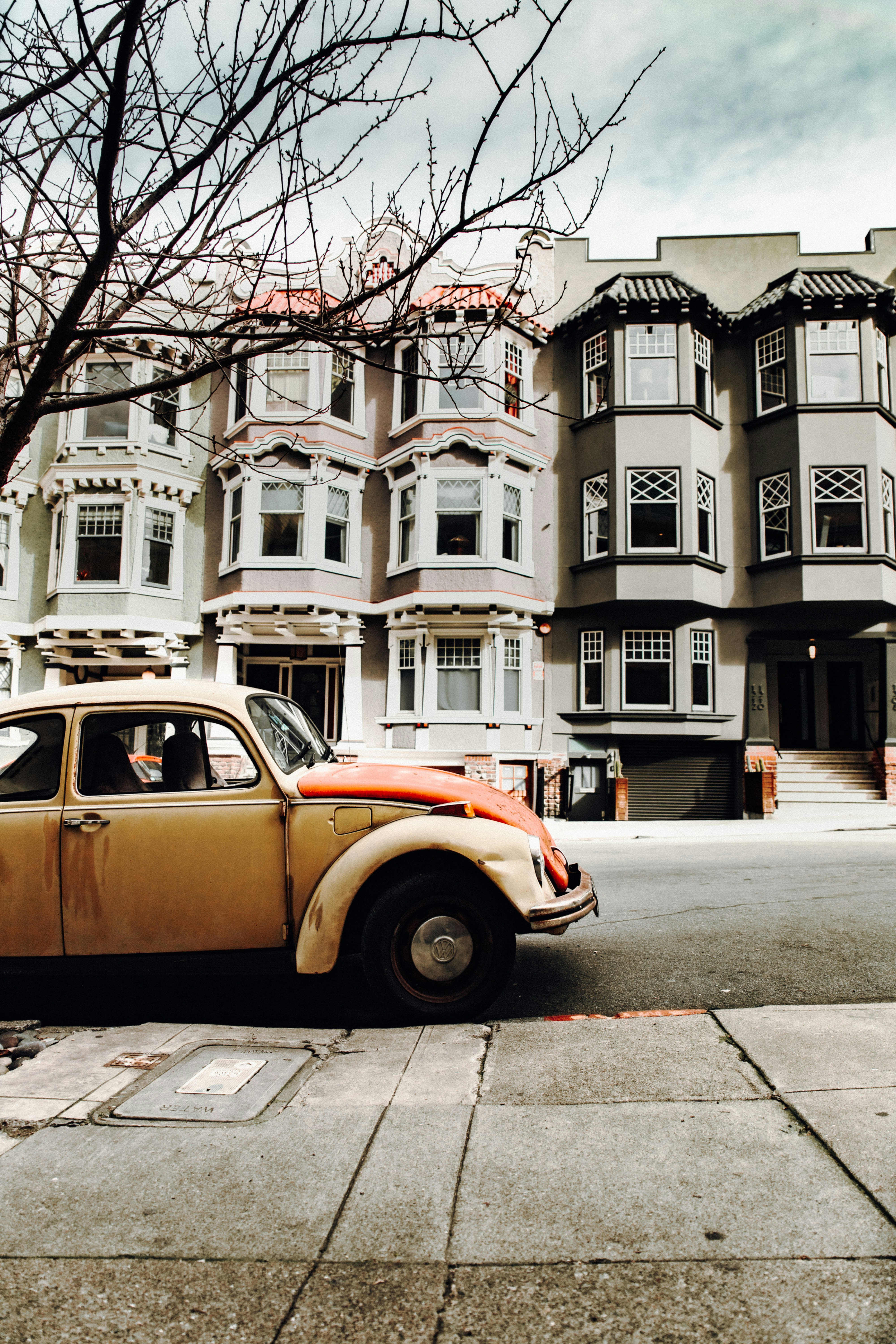 Classic yellow Volkswagen Beetle parked beside ornate historic buildings in an urban setting.