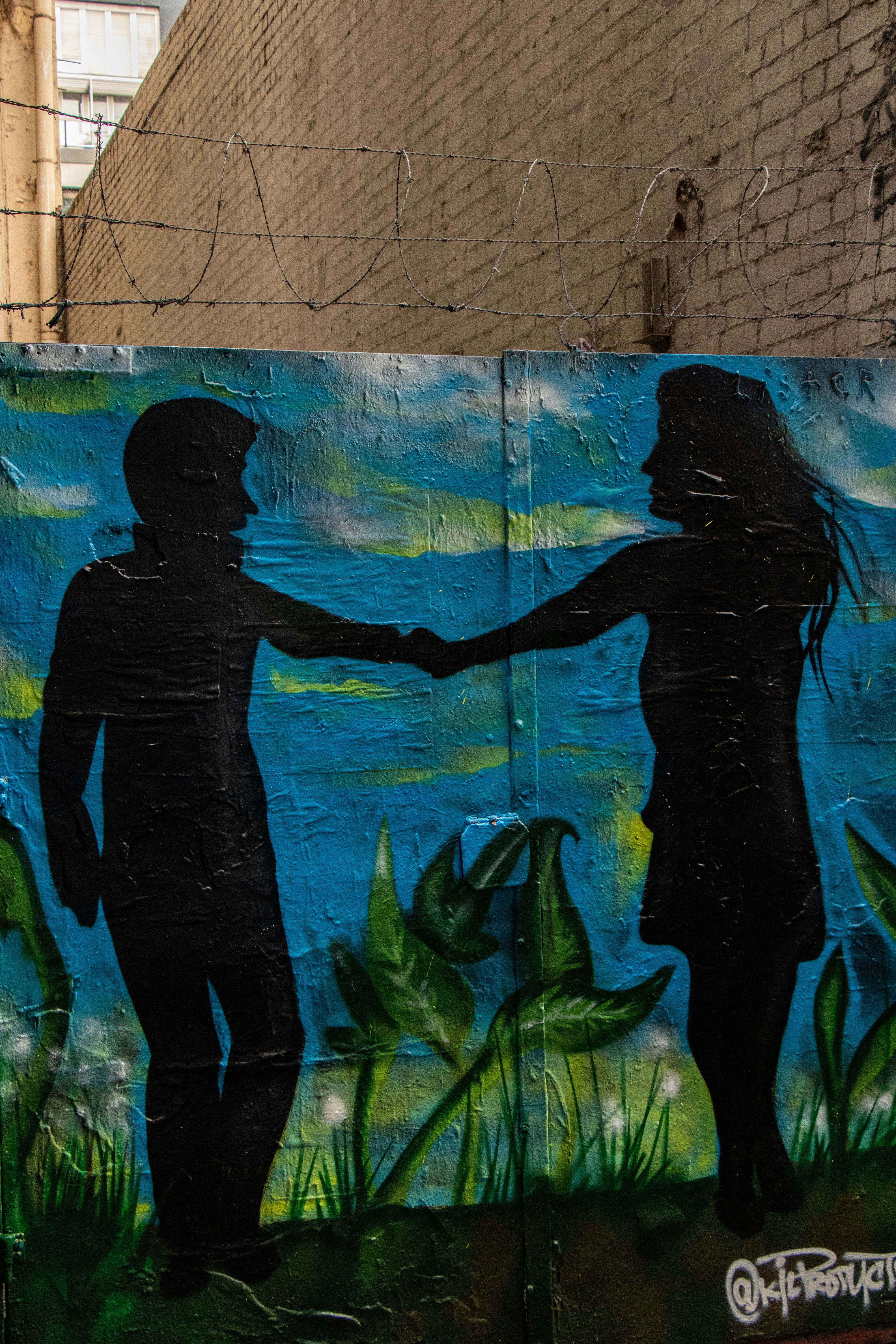 Two Silhouettes Reach Across a Painted Fence
