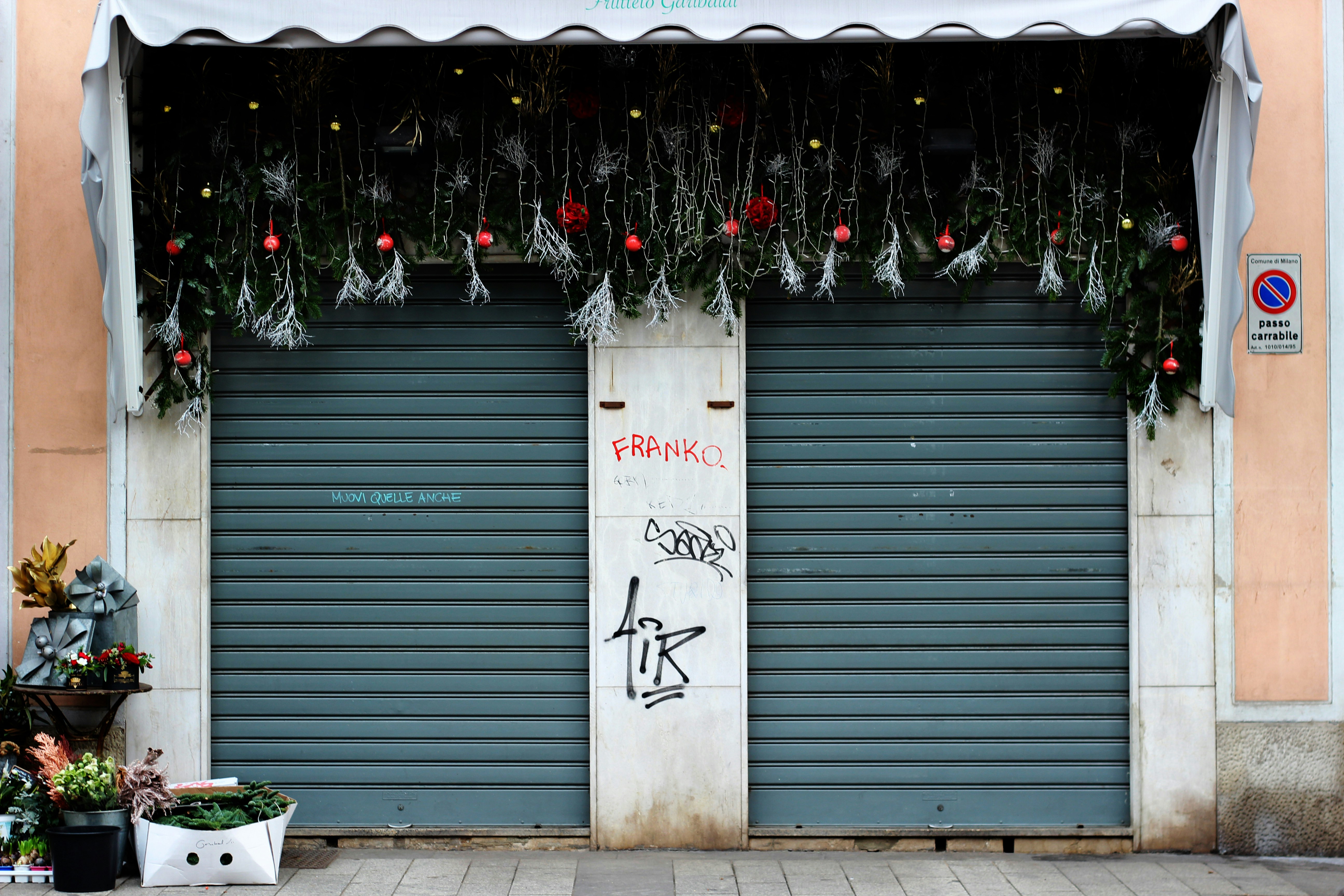 Centre-Panel Graffiti Framed by Holiday Garlands on a Closed Shutter Shopfront