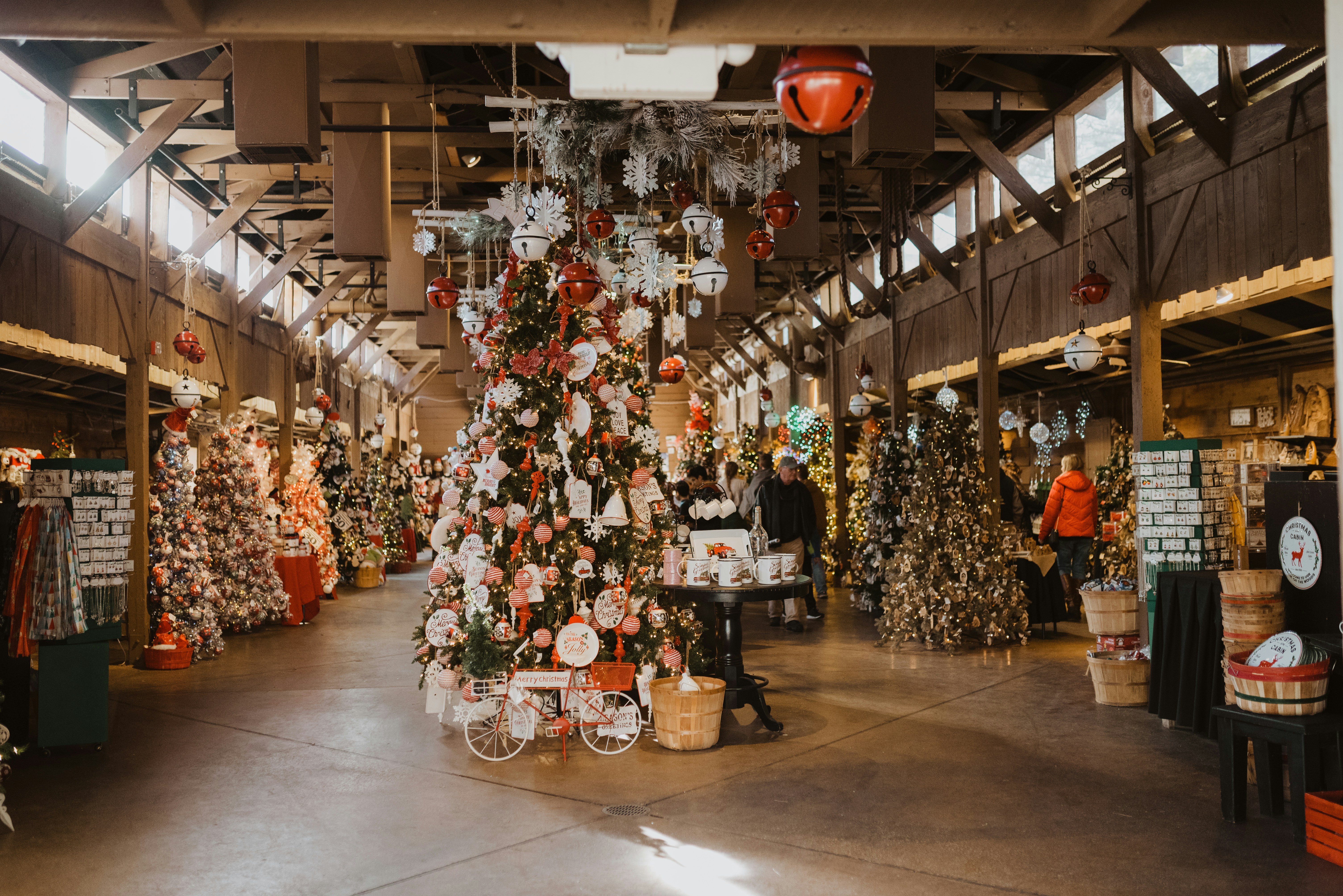 Decorated Christmas trees line a spacious indoor market with wooden beams and soft natural lighting.